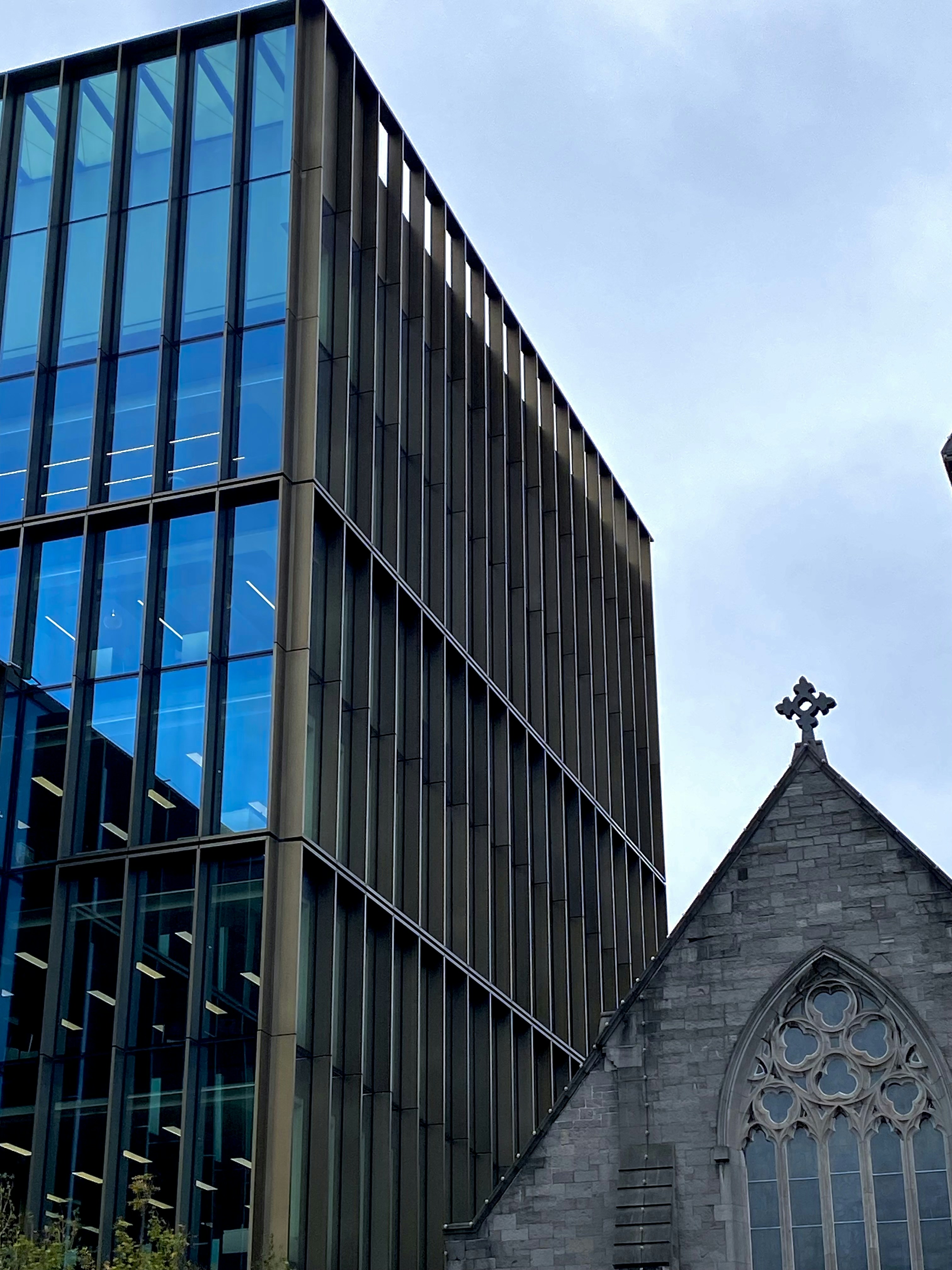 A juxtaposition of a contemporary glass building alongside a historic stone church, showcasing architectural diversity. The scene captures the blend of old and new in urban design.