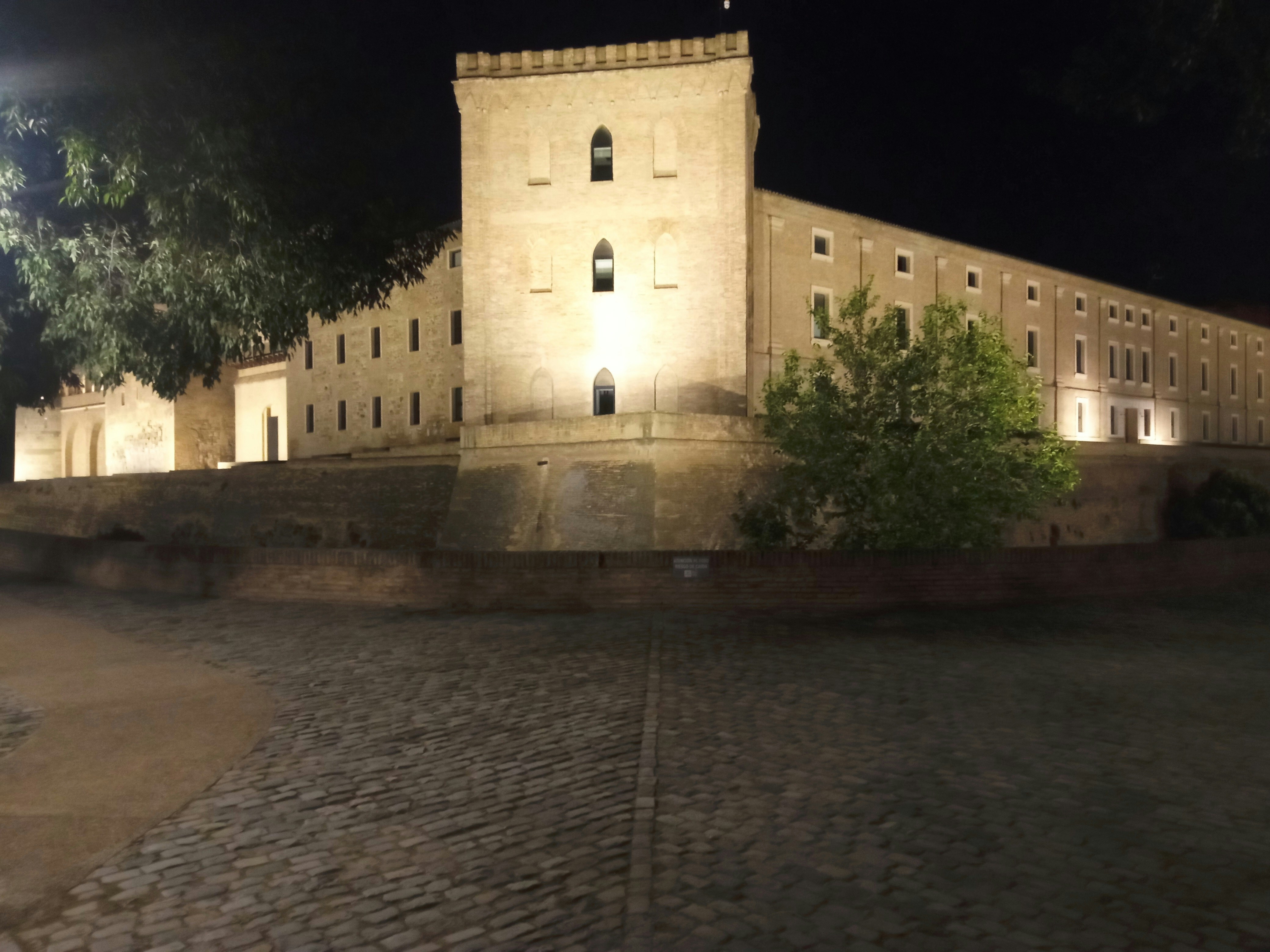 Historic stone building with illuminated facade and towering presence on a cobblestone road at night.