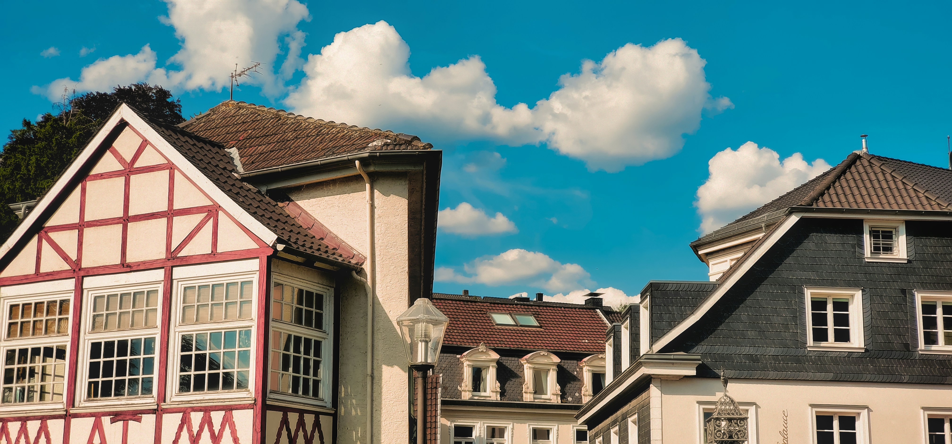 Traditional houses with pitched roofs set against a vibrant blue sky dotted with fluffy clouds.