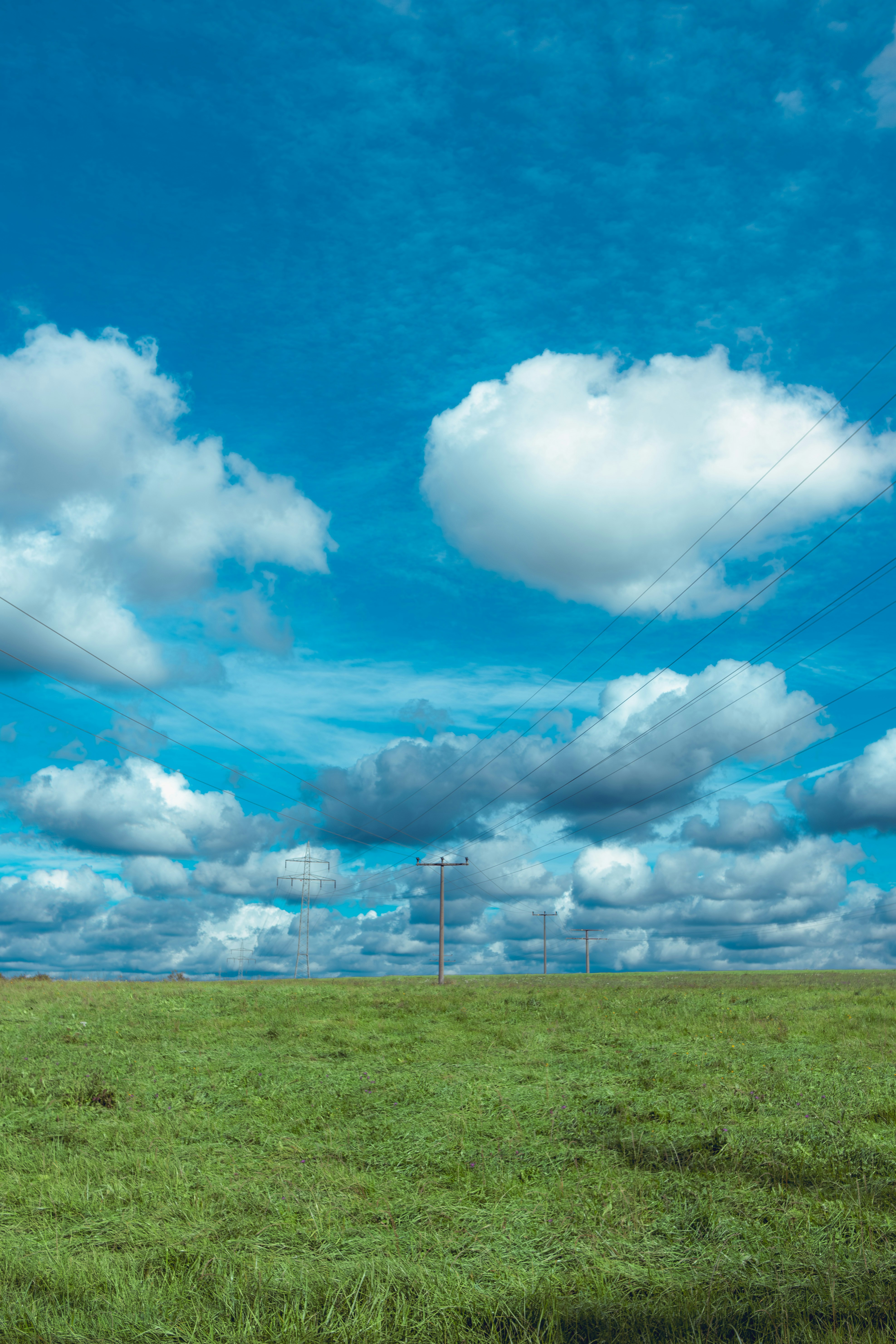 Power Lines Crossing a Quiet Prairie Under a Cloudy Blue Sky