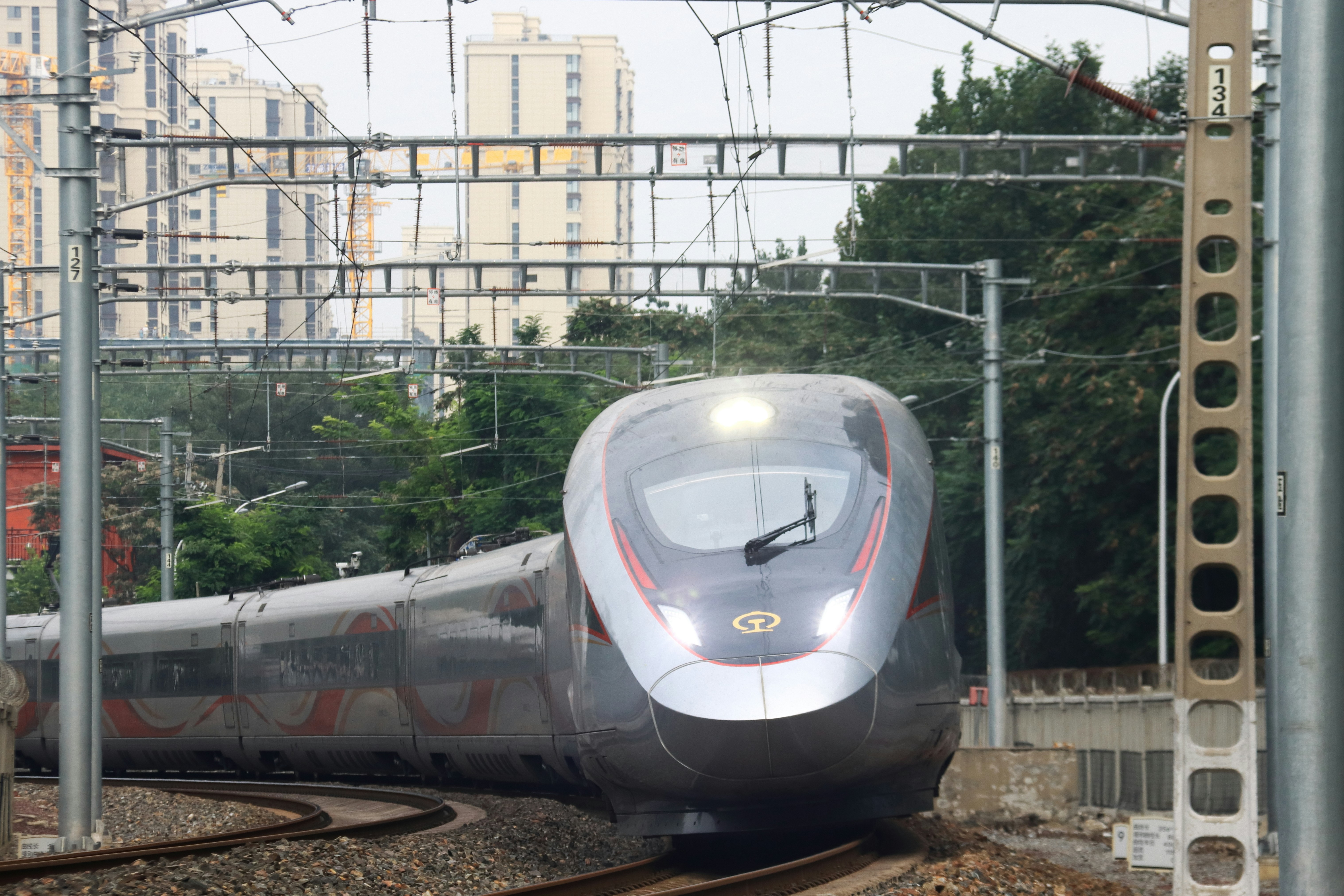 A silver train traveling down train tracks next to tall buildings photo ...