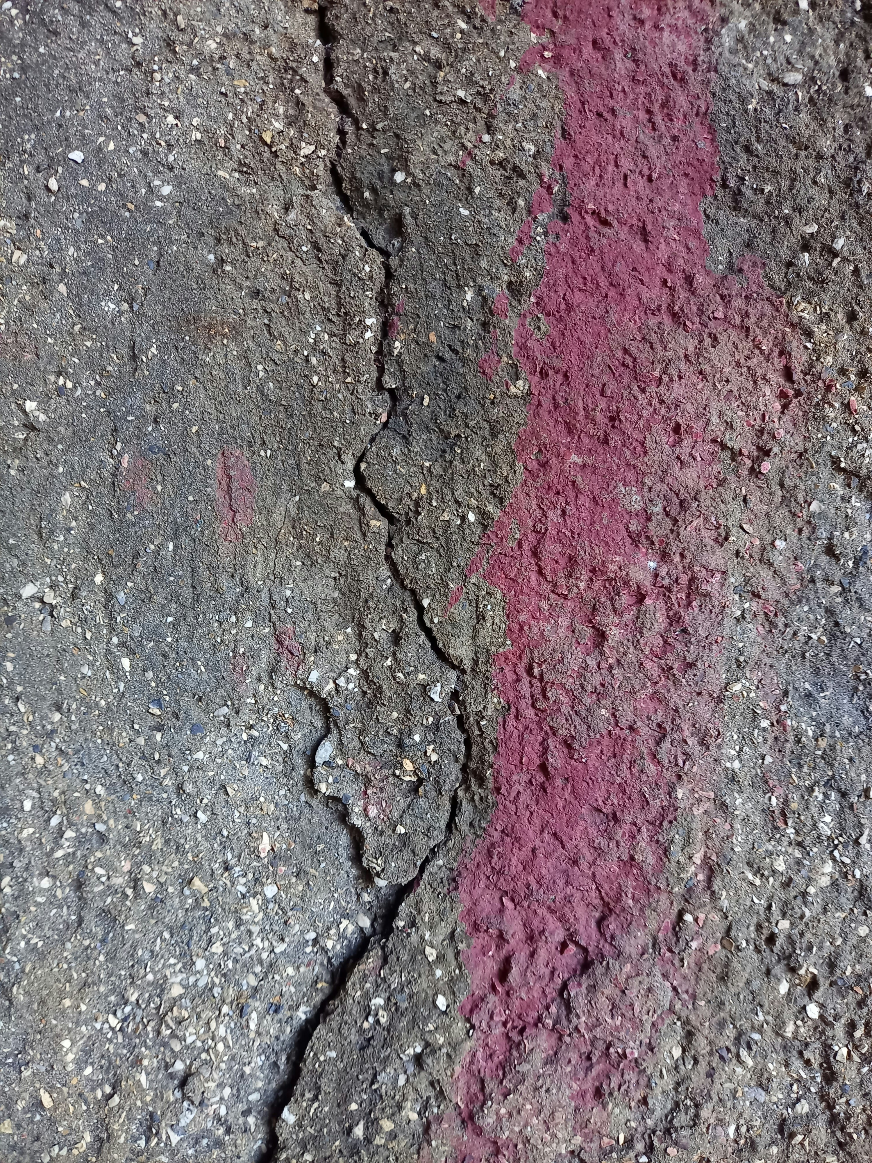 Close-up view of cracked concrete with a vibrant red streak, showcasing the textures and imperfections of the surface.