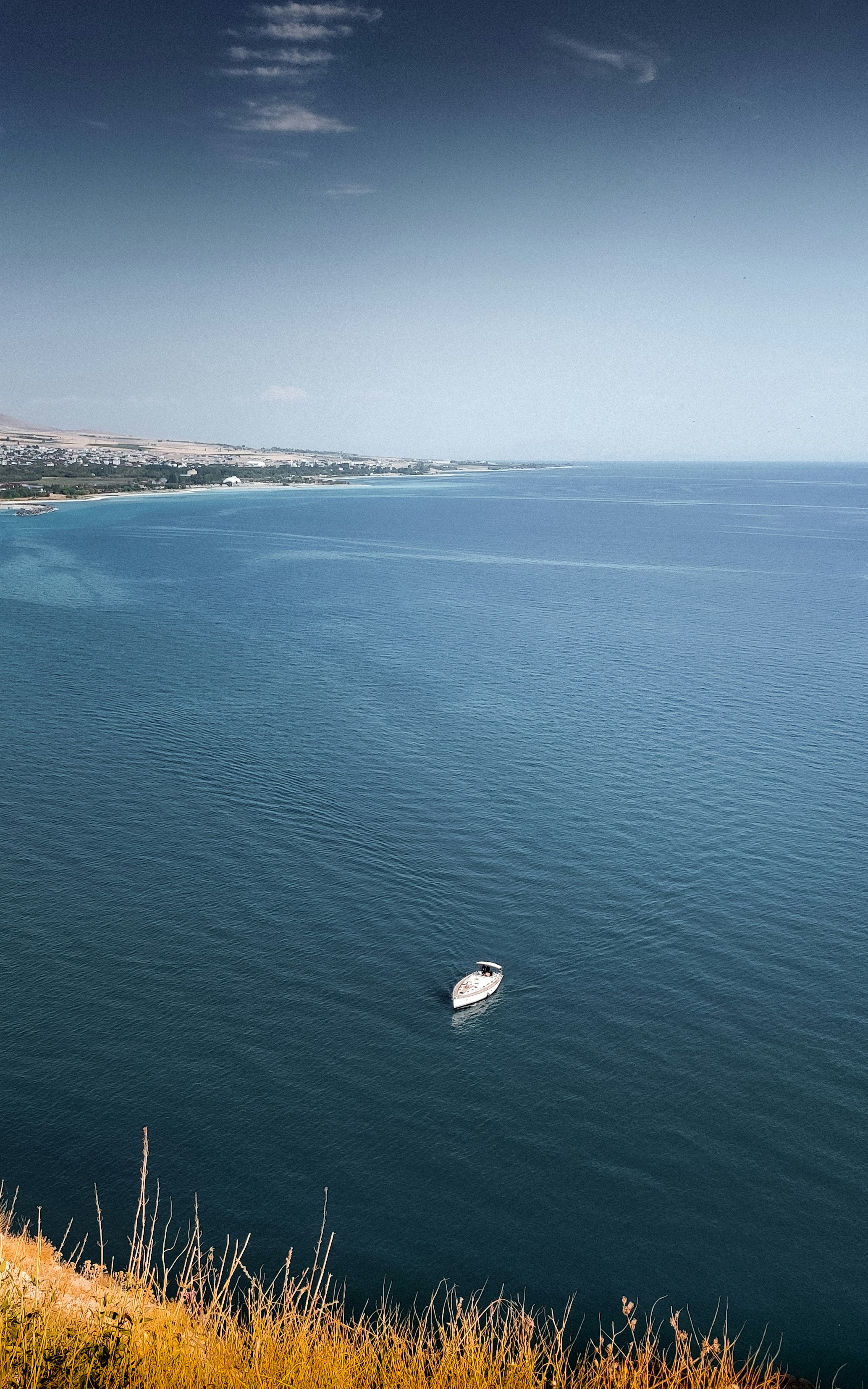 White boat on expansive blue lake with distant shoreline under a clear sky.