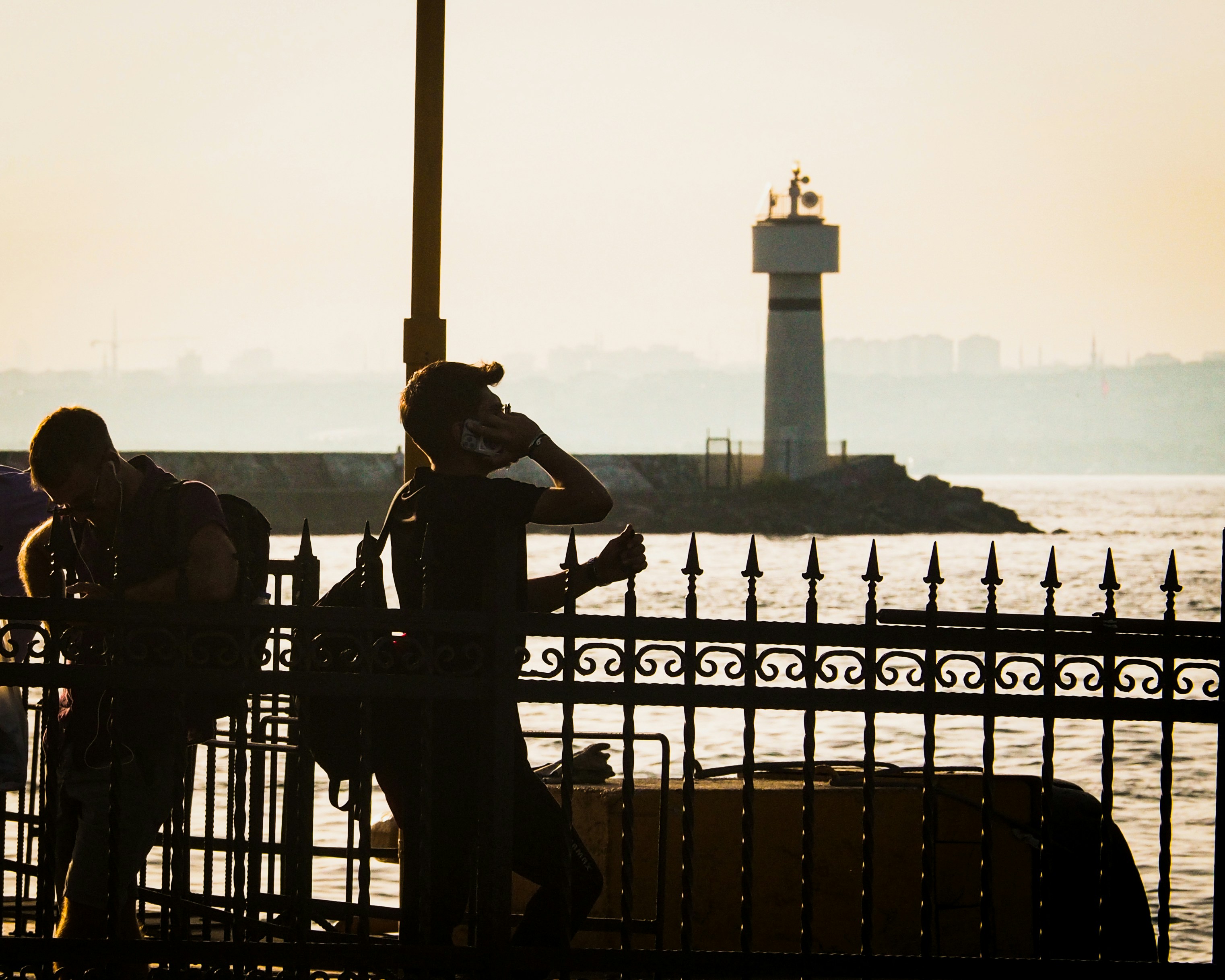 Dusk Silhouettes by the Harbor Fence with a Distant Lighthouse
