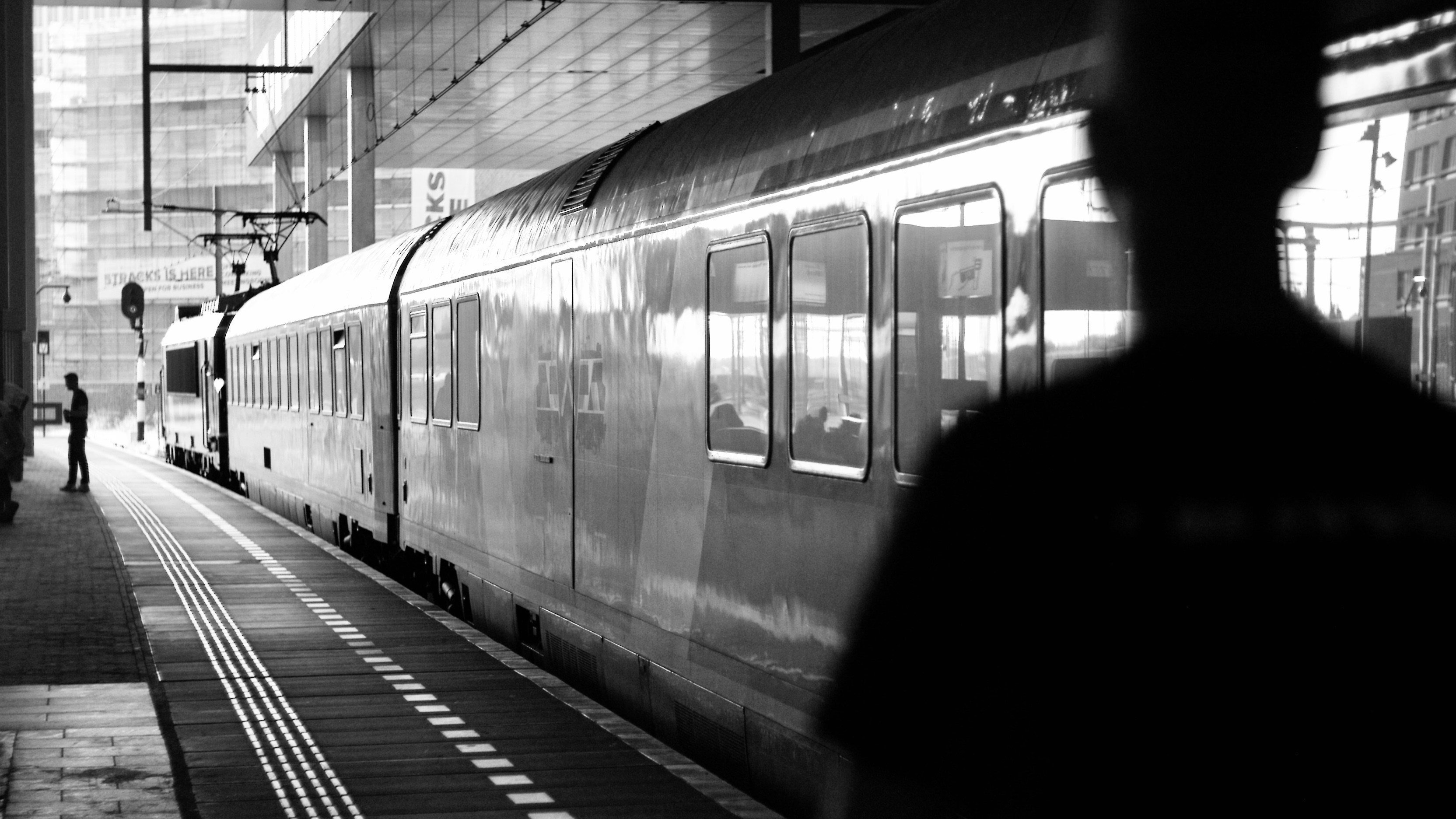 Silhouette of a person standing near a train at a modern station, with strong contrasts in black and white.