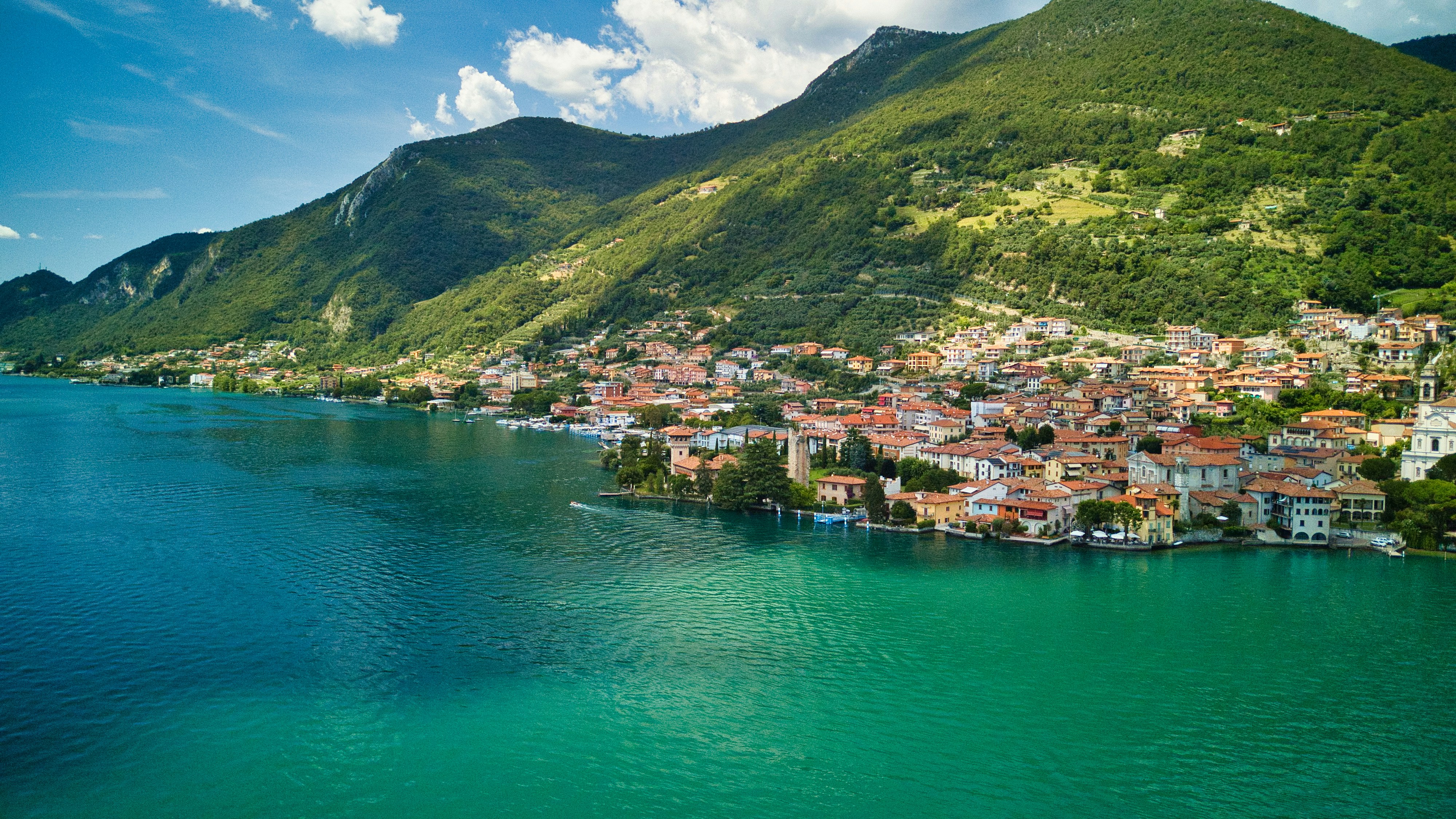 Aerial view of a coastal village nestled against lush green hills with vibrant blue waters in the foreground.