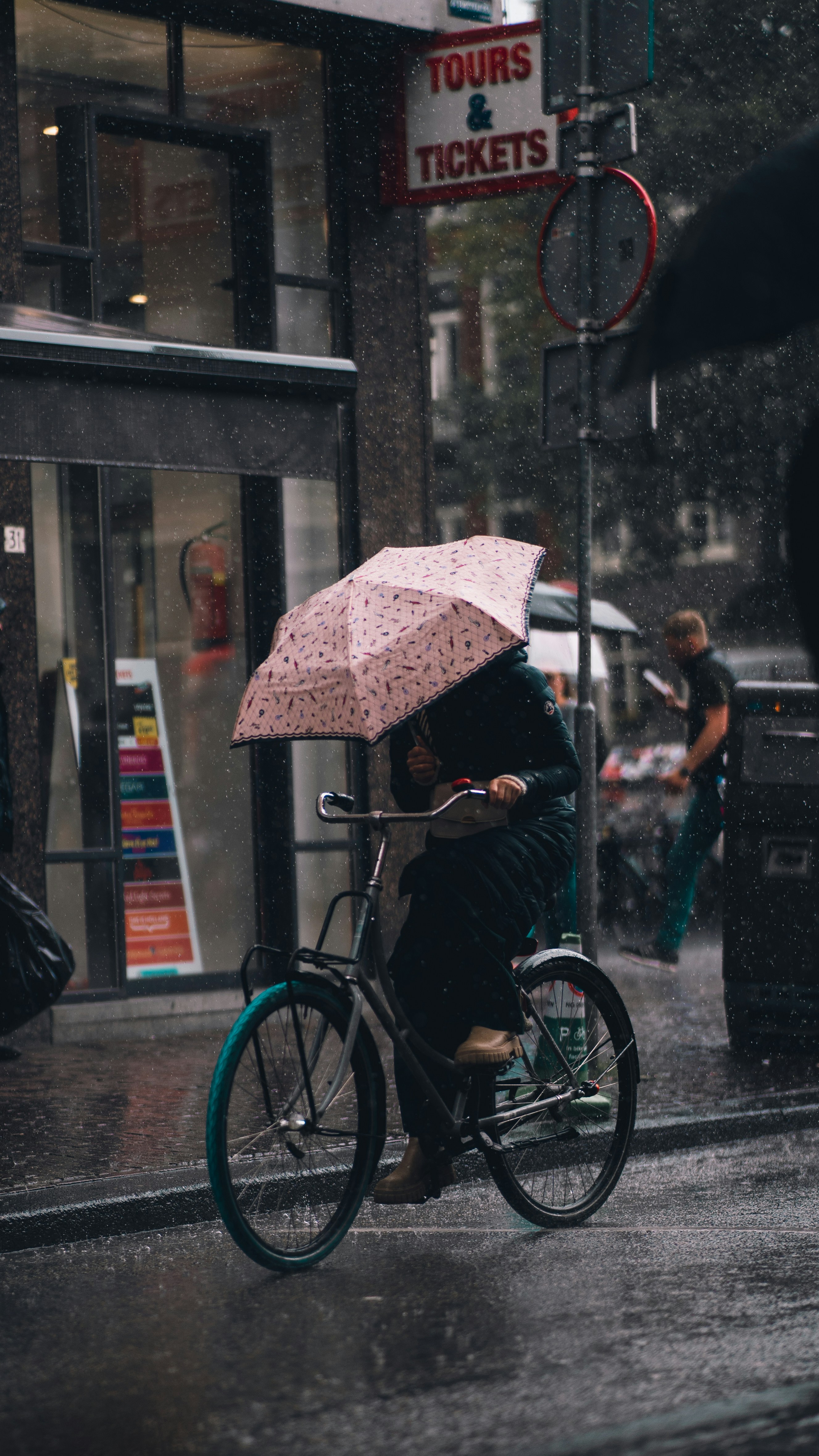 Rainy Street Portrait: A Teal-Wheeled Cyclist Under a Pink Polka-Dot Umbrella