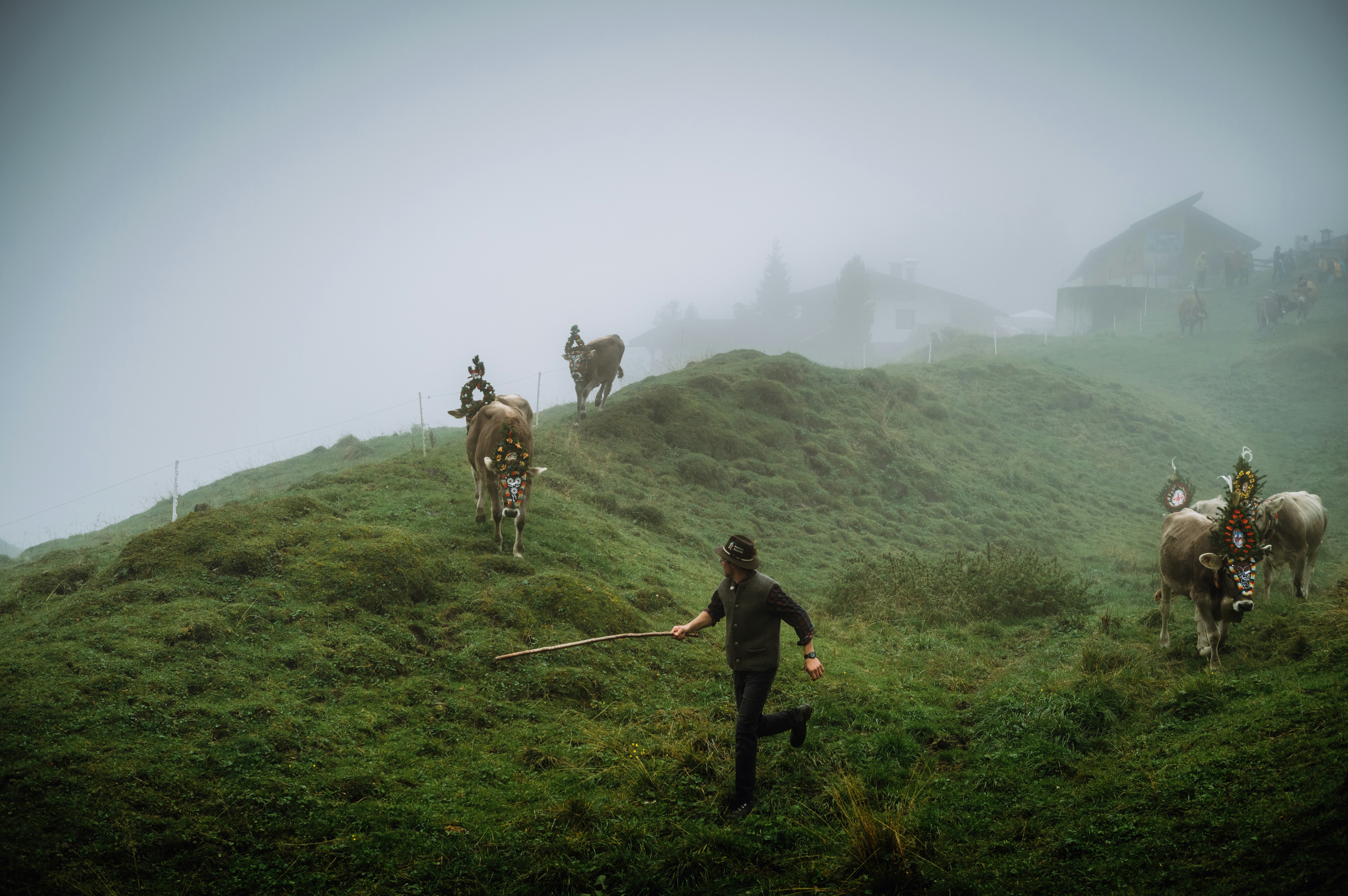 A lone swordsman runs with a drawn blade across a damp, grassy hillside. Riders on horseback fade into the fog behind him.