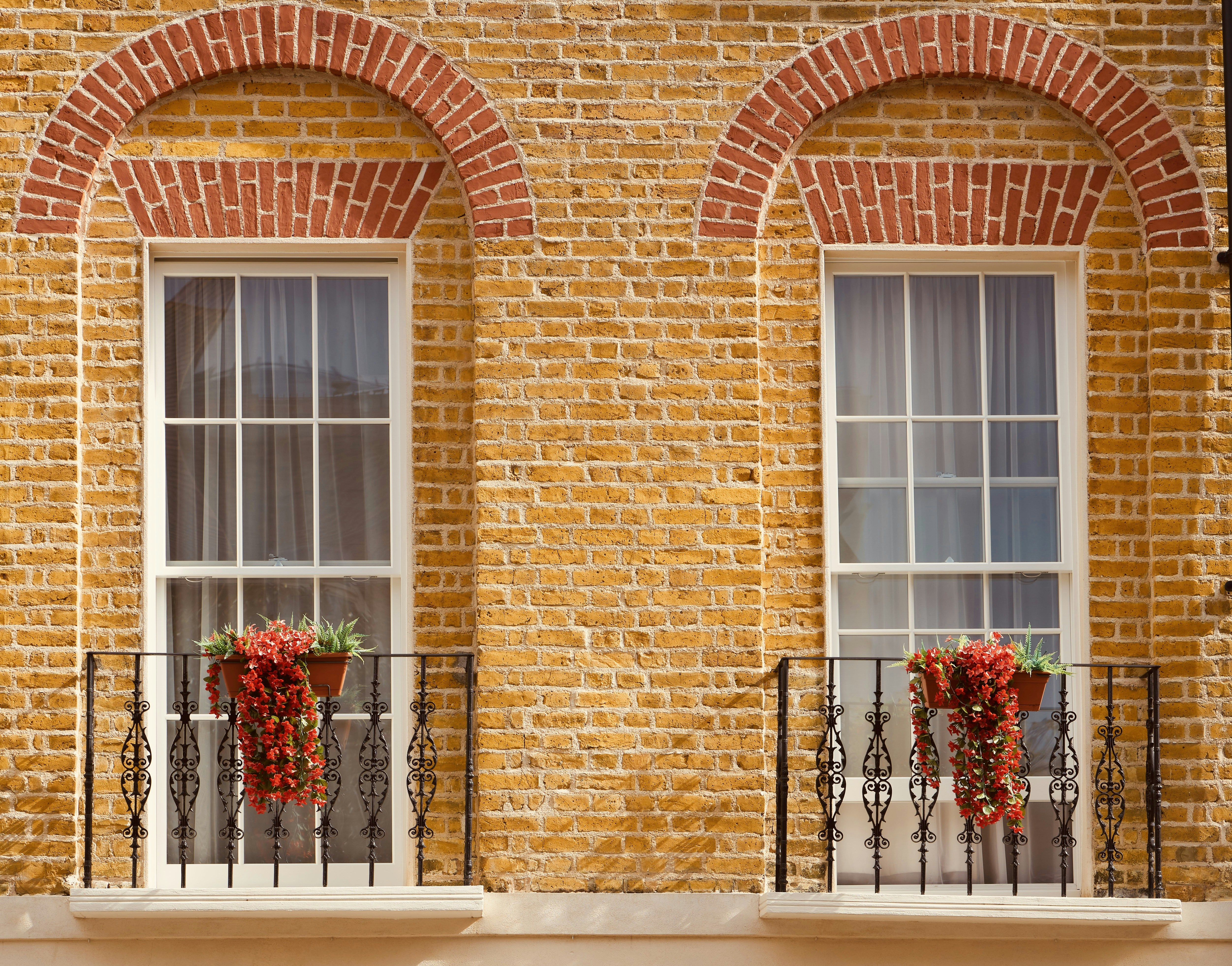 Balanced Charm: Twin Windows with Flowering Banners Against Brickwork