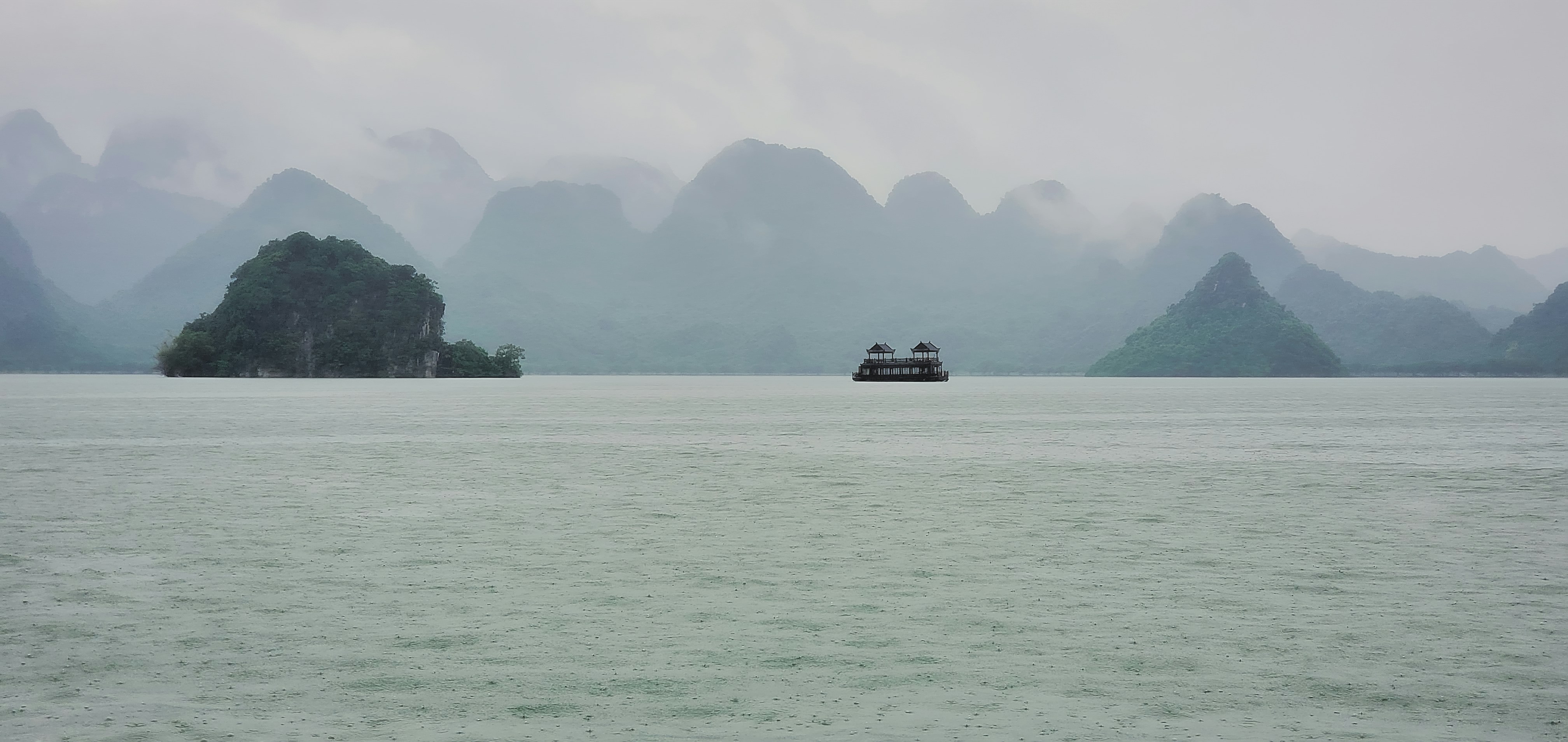 Boat navigating tranquil waters with mist-shrouded islands in the distance.