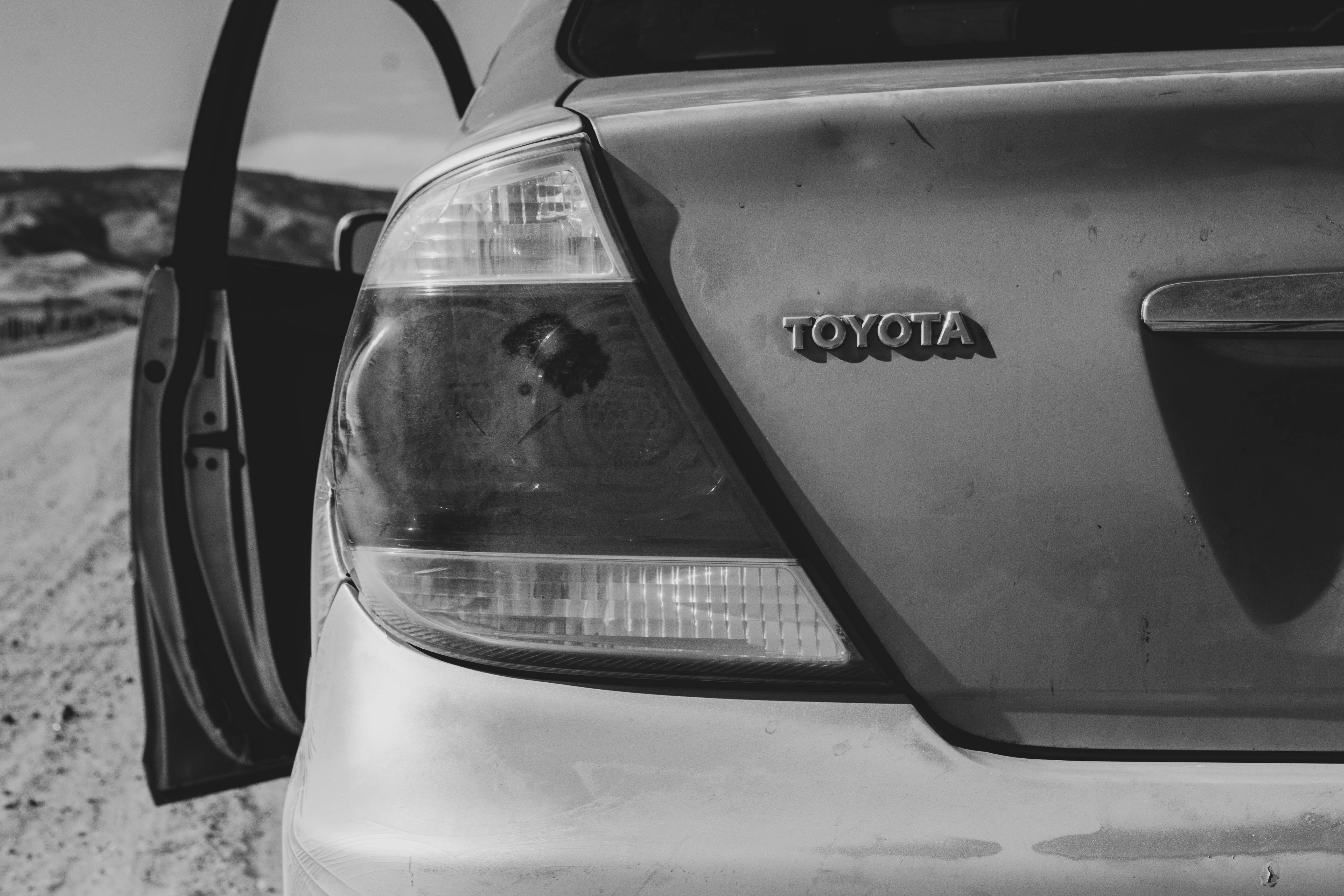Monochrome Close-Up: Toyota Emblem and Taillight Across a Desert Dune Backdrop