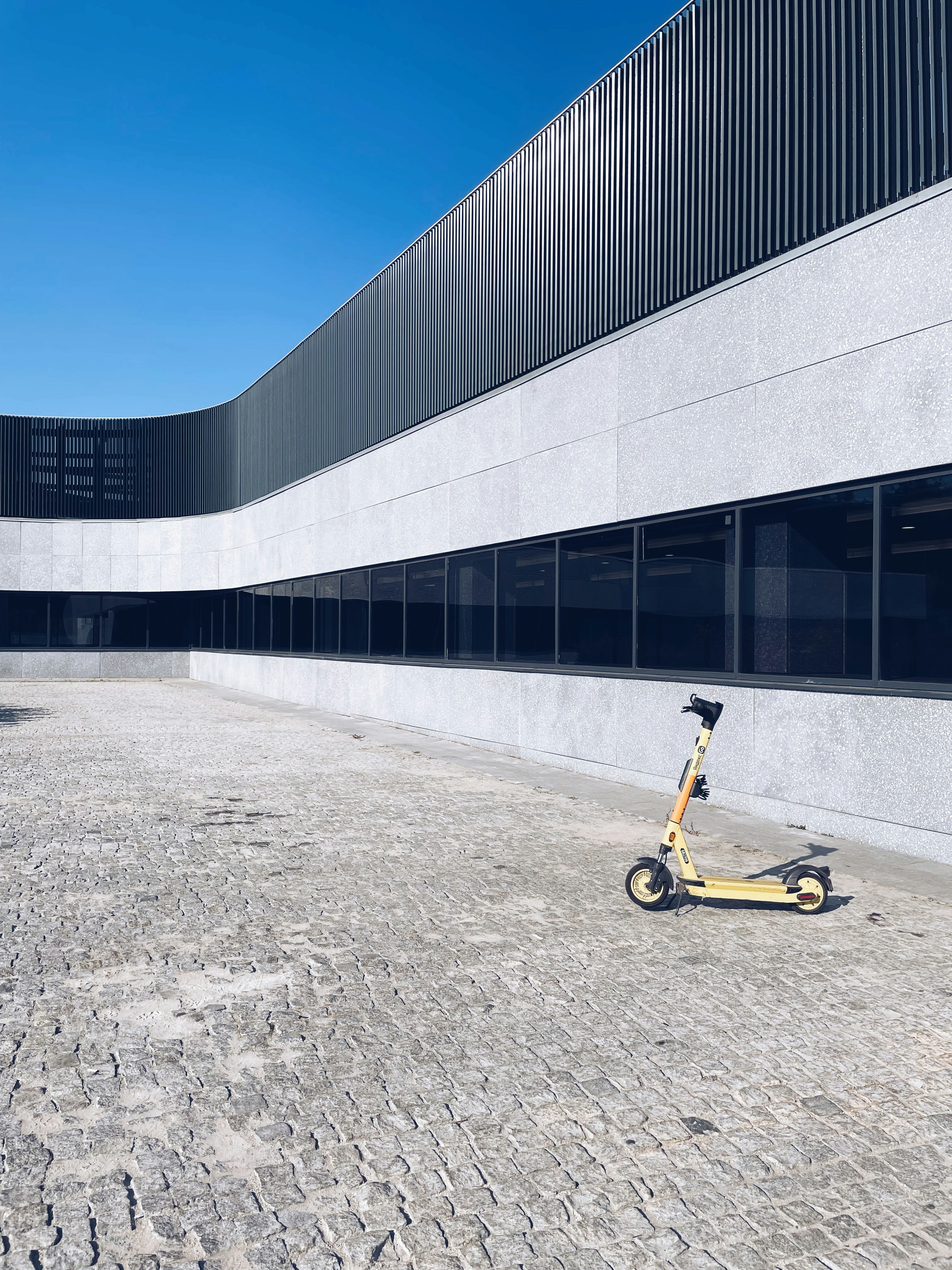 Sunlit Geometry: A Yellow Scooter at the Edge of a Modern Campus Facade