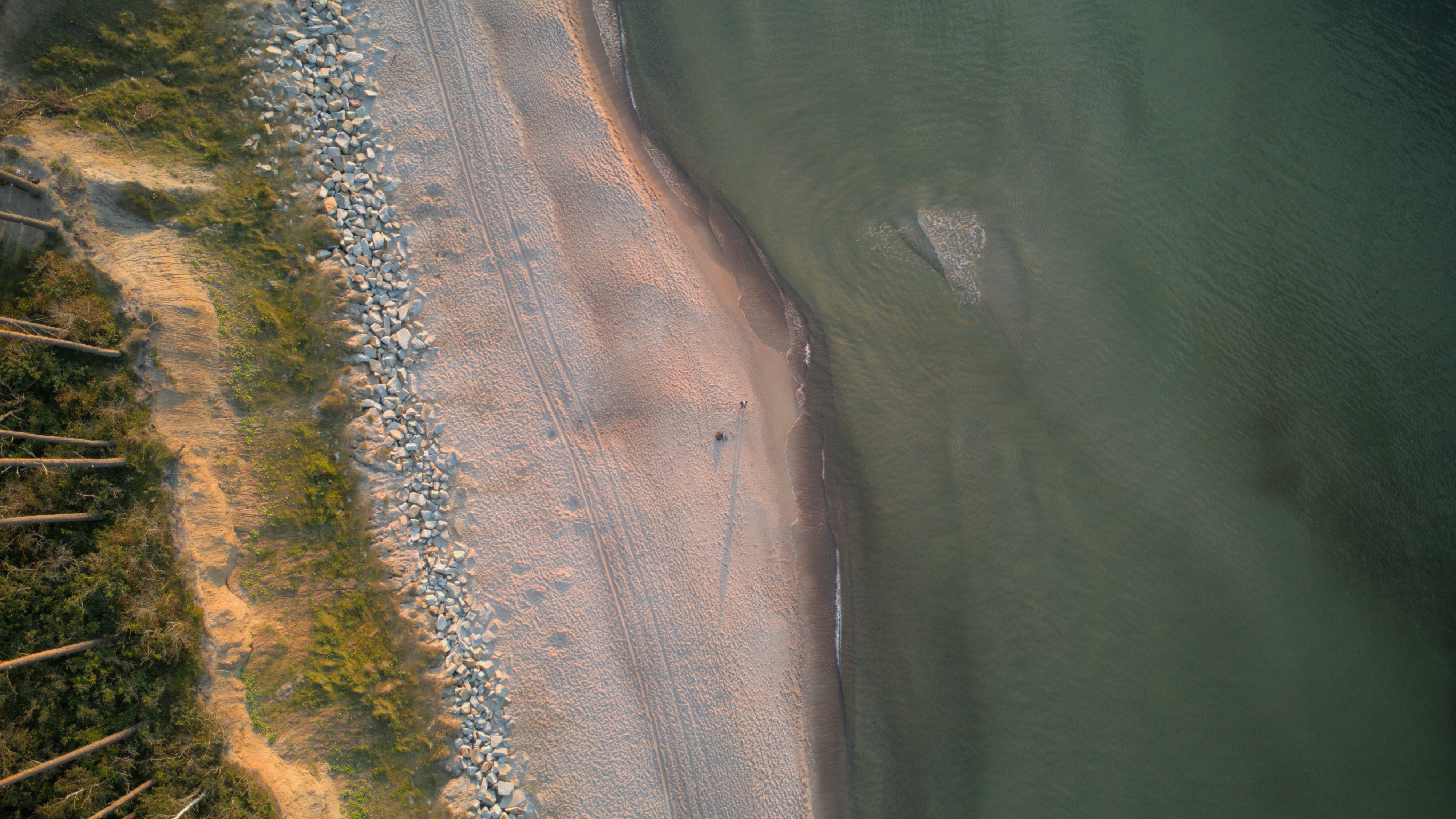 Aerial view of a serene beach with gentle waves lapping at the shore, framed by lush greenery and rocky formations. The scene captures the harmony of land and sea.