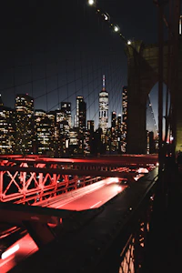 Crimson Veins Over a Night Skyline: Traffic Streams Beneath the Brooklyn Bridge
