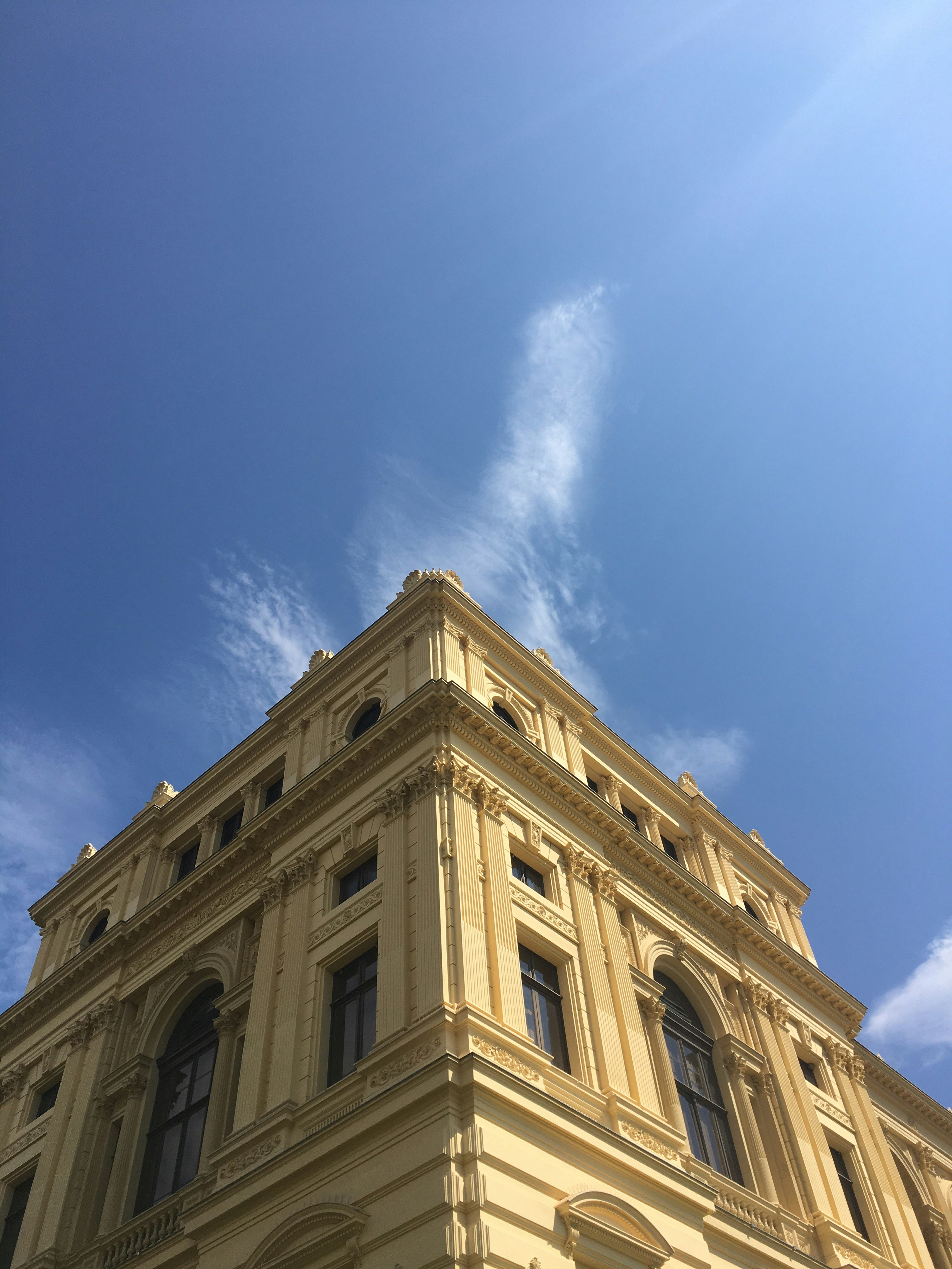 Golden building facade reaching towards a bright blue sky with wispy clouds.