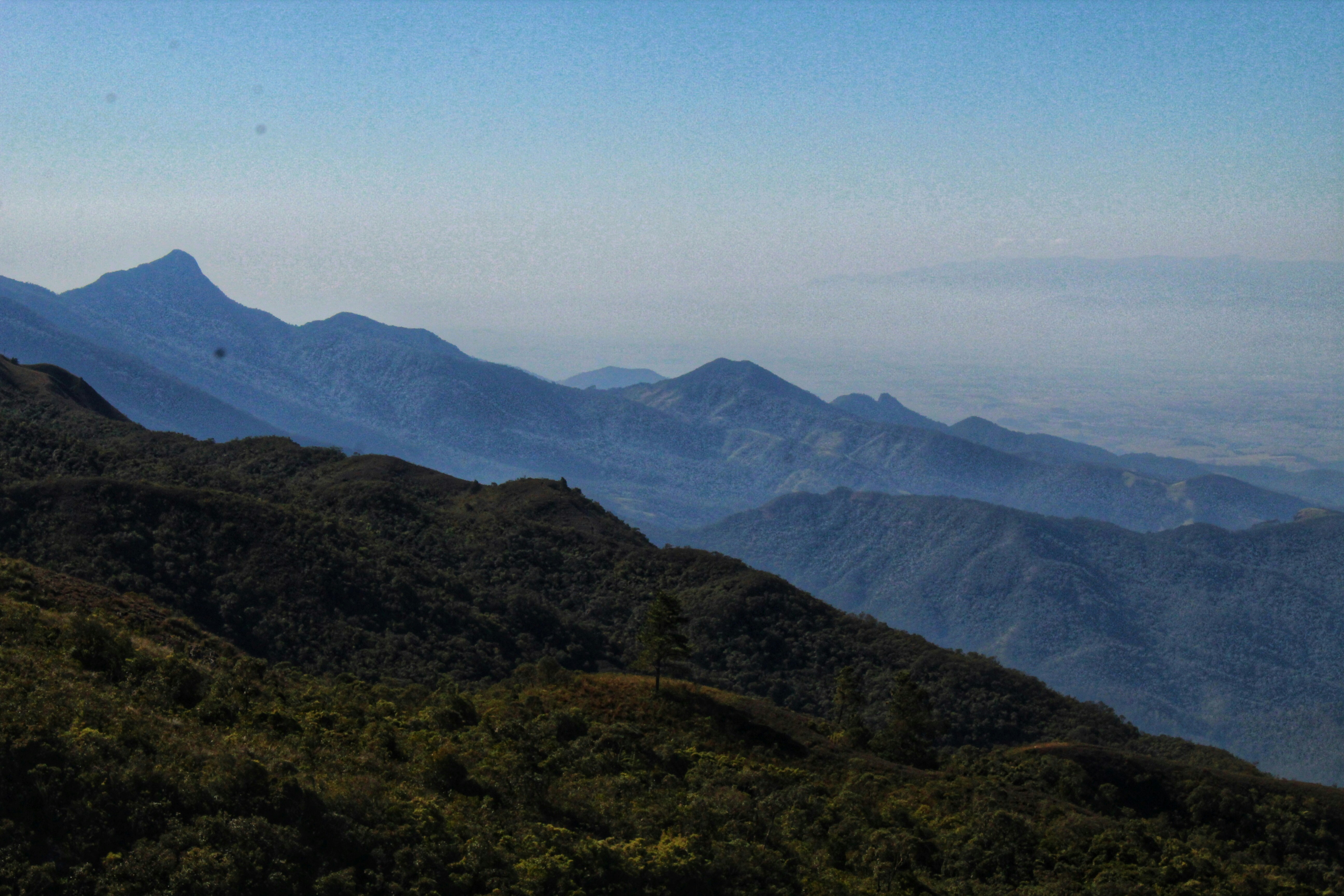 Misty mountain ranges extending into the horizon beneath a clear blue sky.