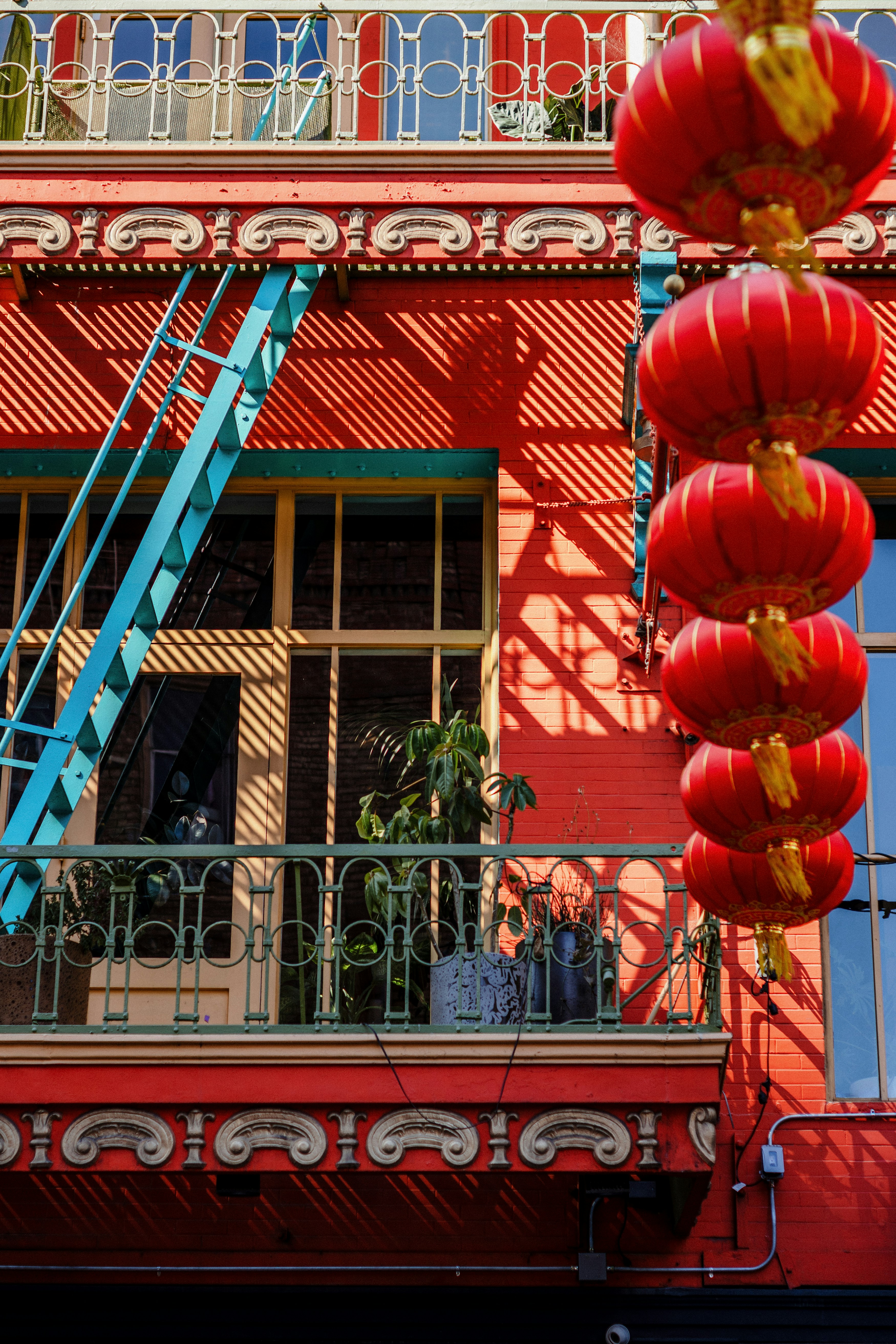 Diagonal Teal Staircase Carves Through a Red Facade Beneath Lanterns