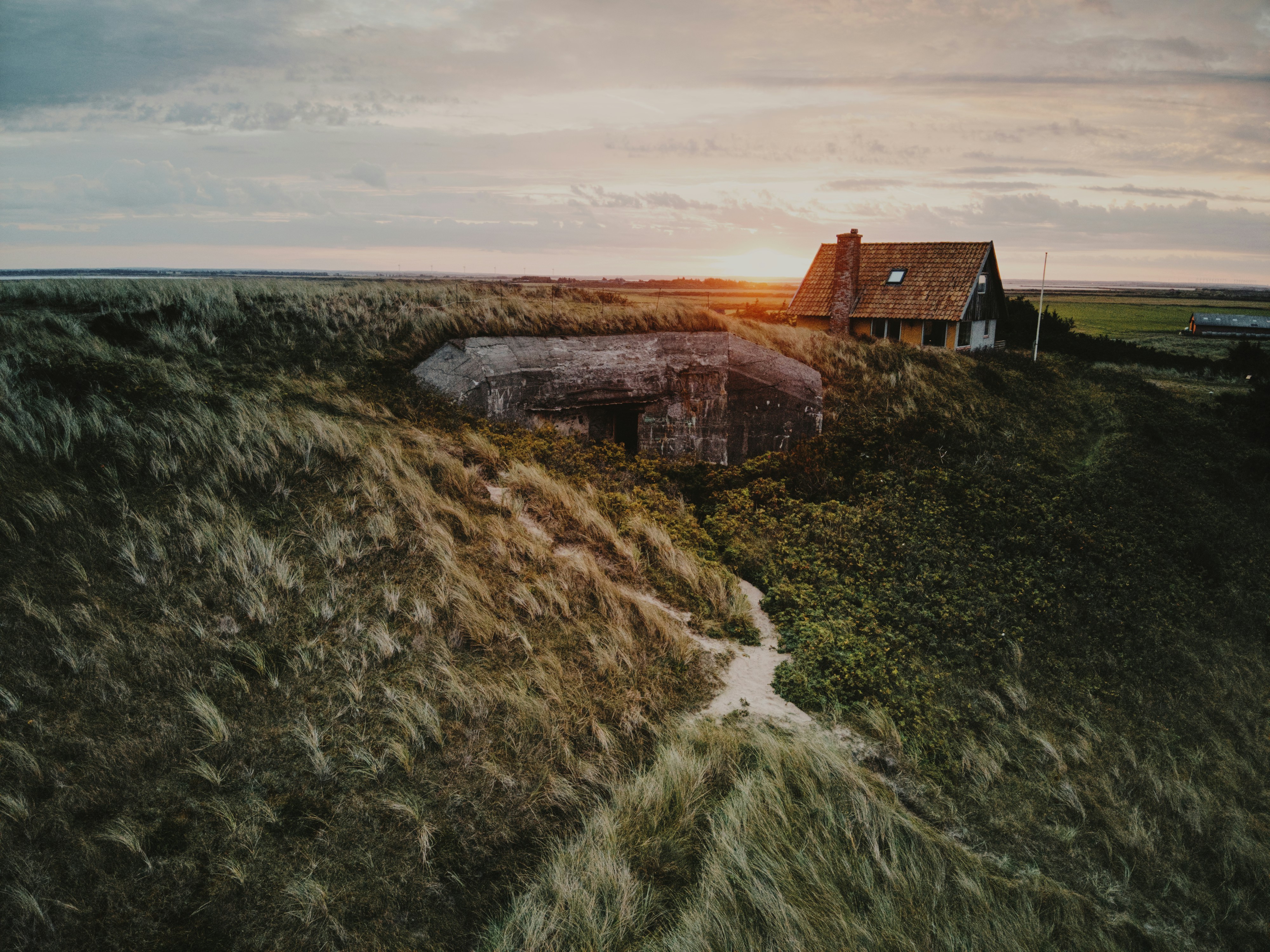 Dusk over the Dune Crest: A Weathered Bunker Beside a Red-Roofed House