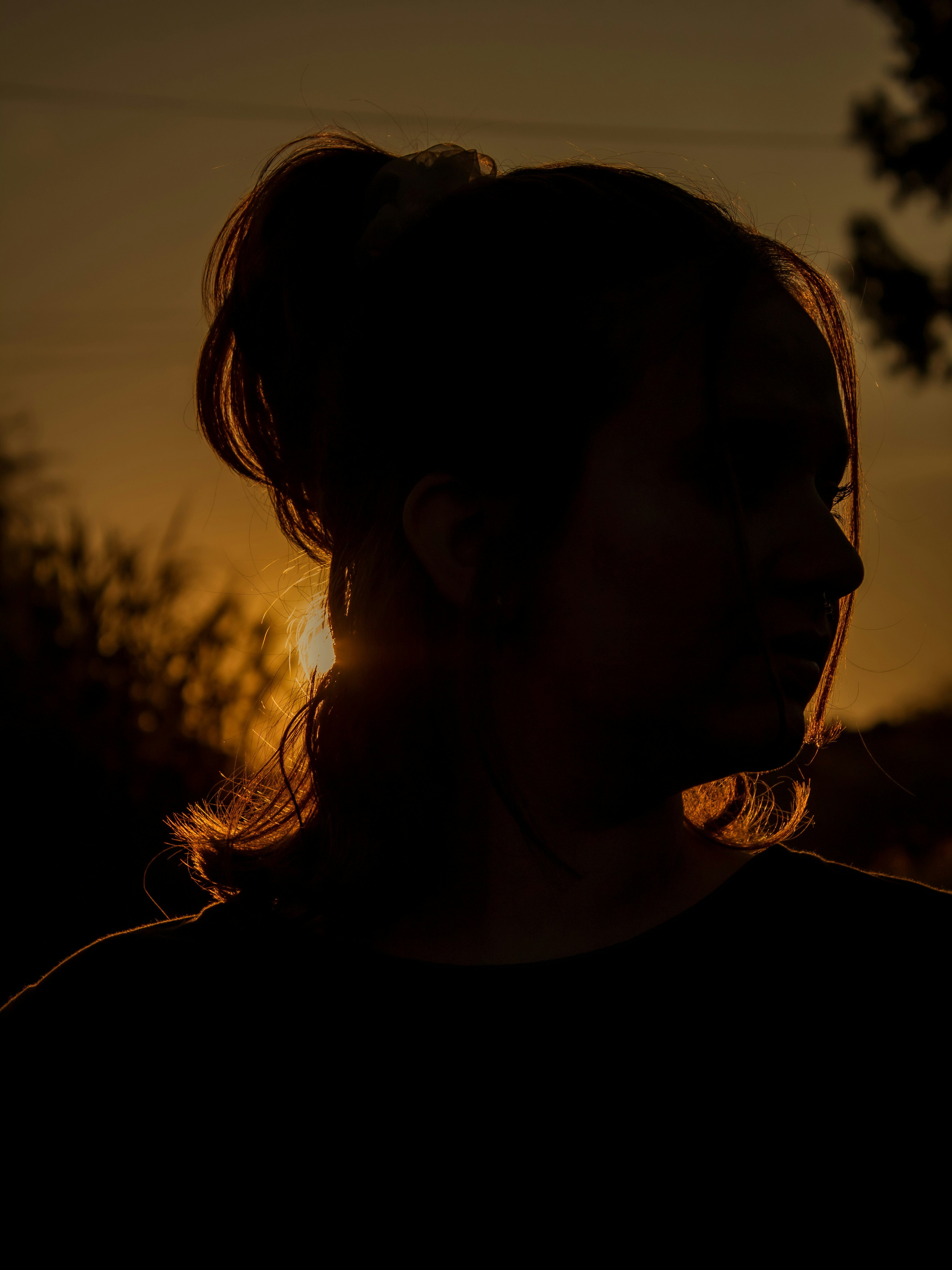 Silhouette of a woman against a vibrant sunset, with glowing light outlining her features.