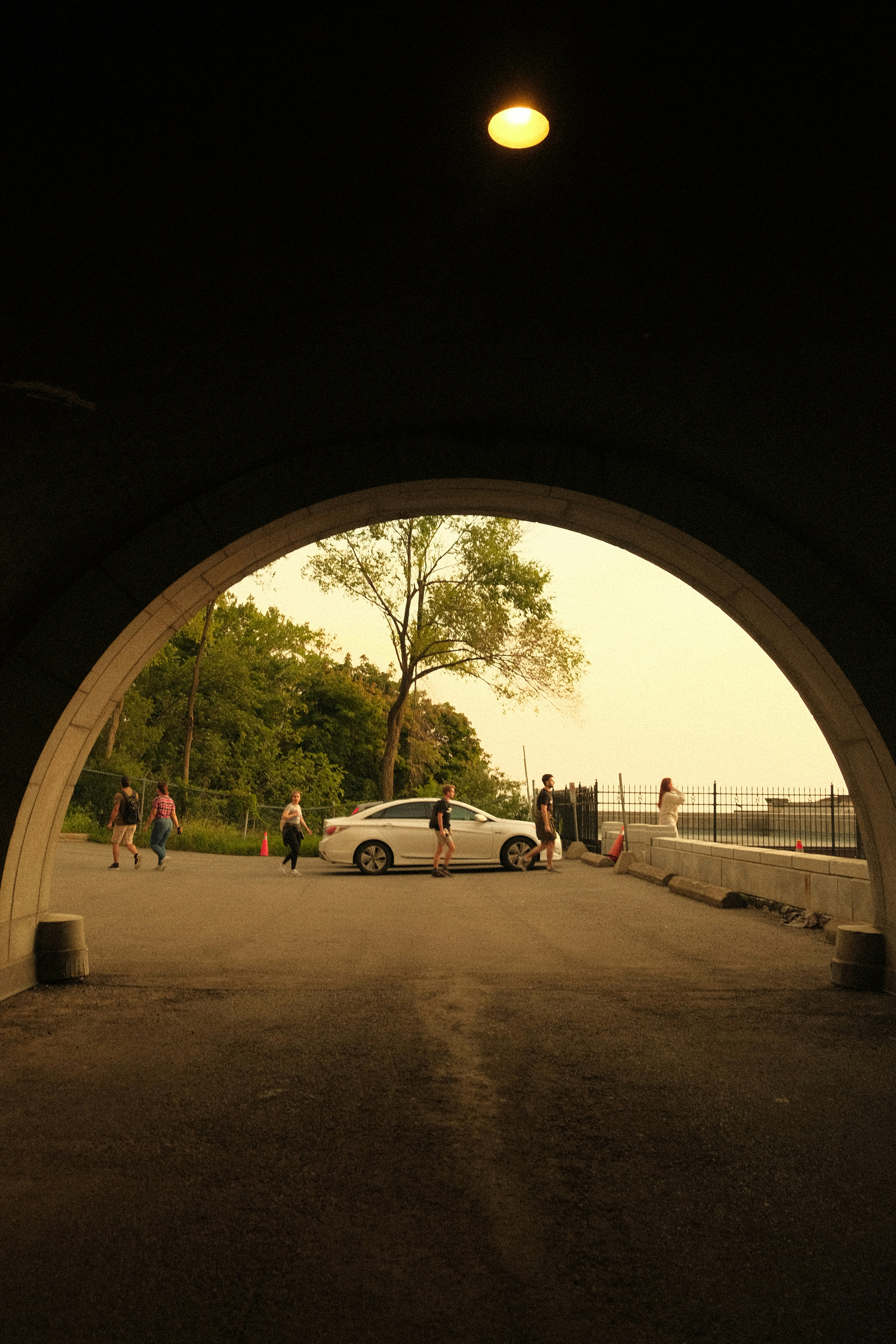 Golden Archway Riverside: Pedestrians and a Car Framed by Evening Light