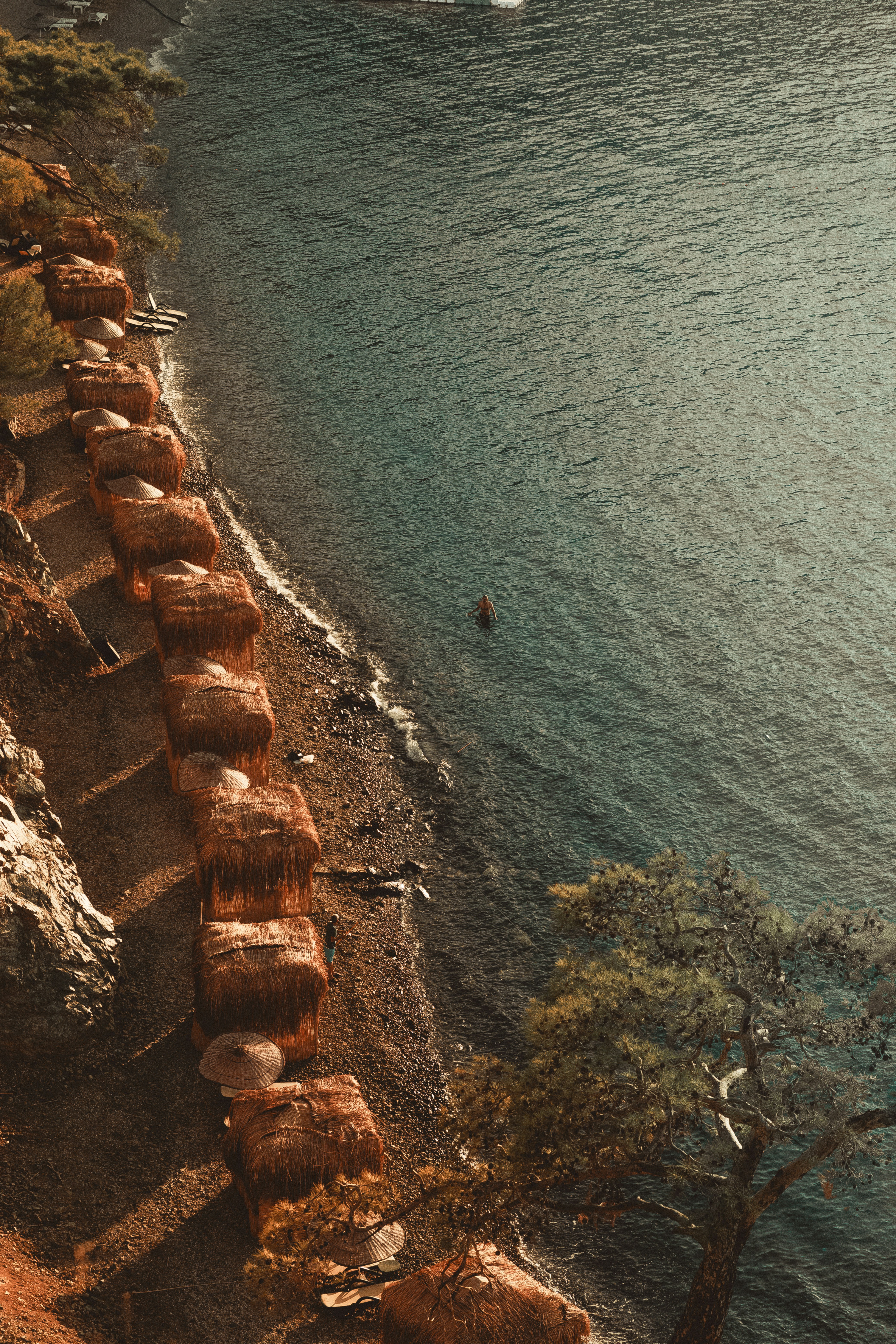 Thatched Cove: Row of Coastal Huts and a Lone Swimmer