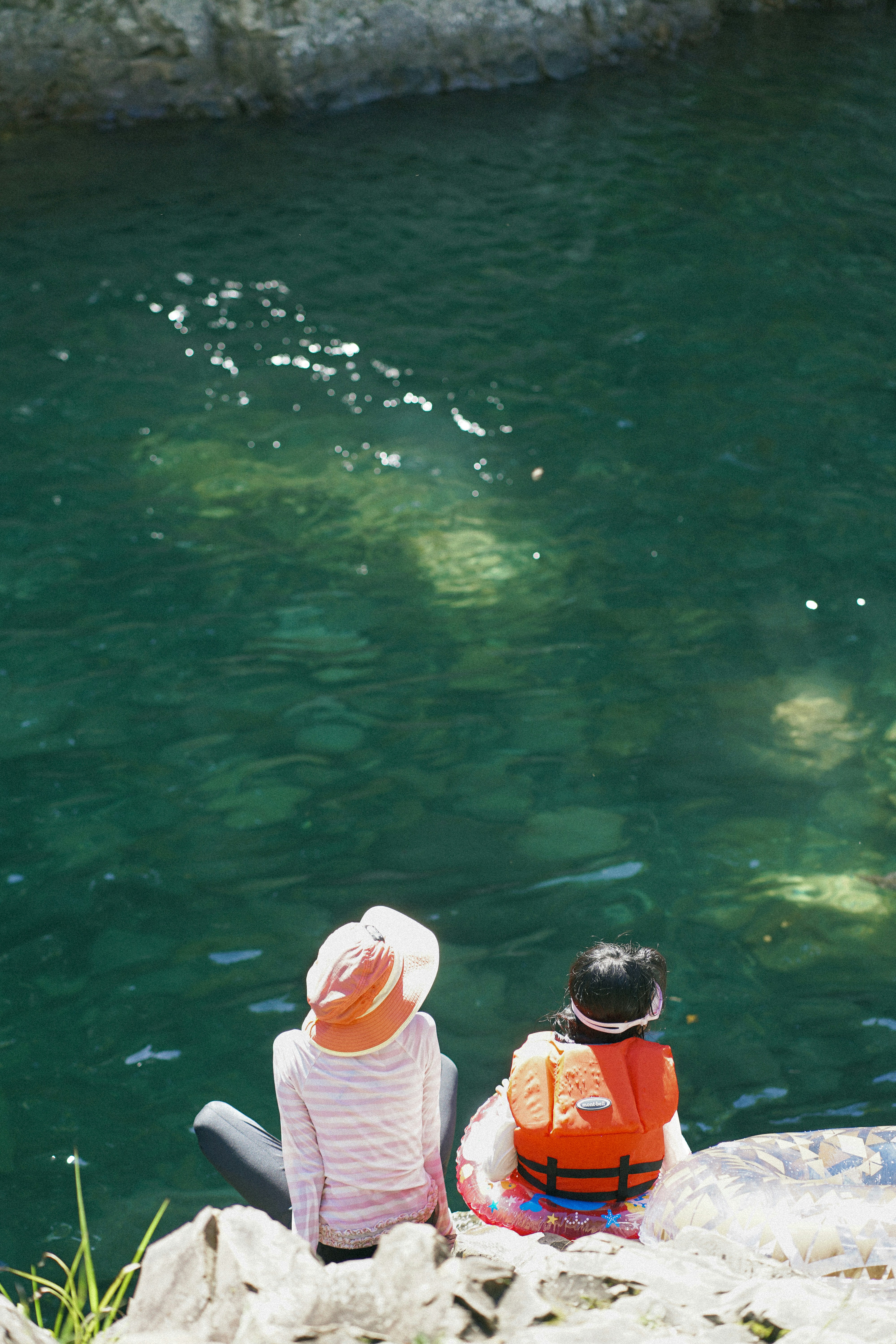 Emerald Edge: Two shoregoers in orange life jackets by a rocky cove