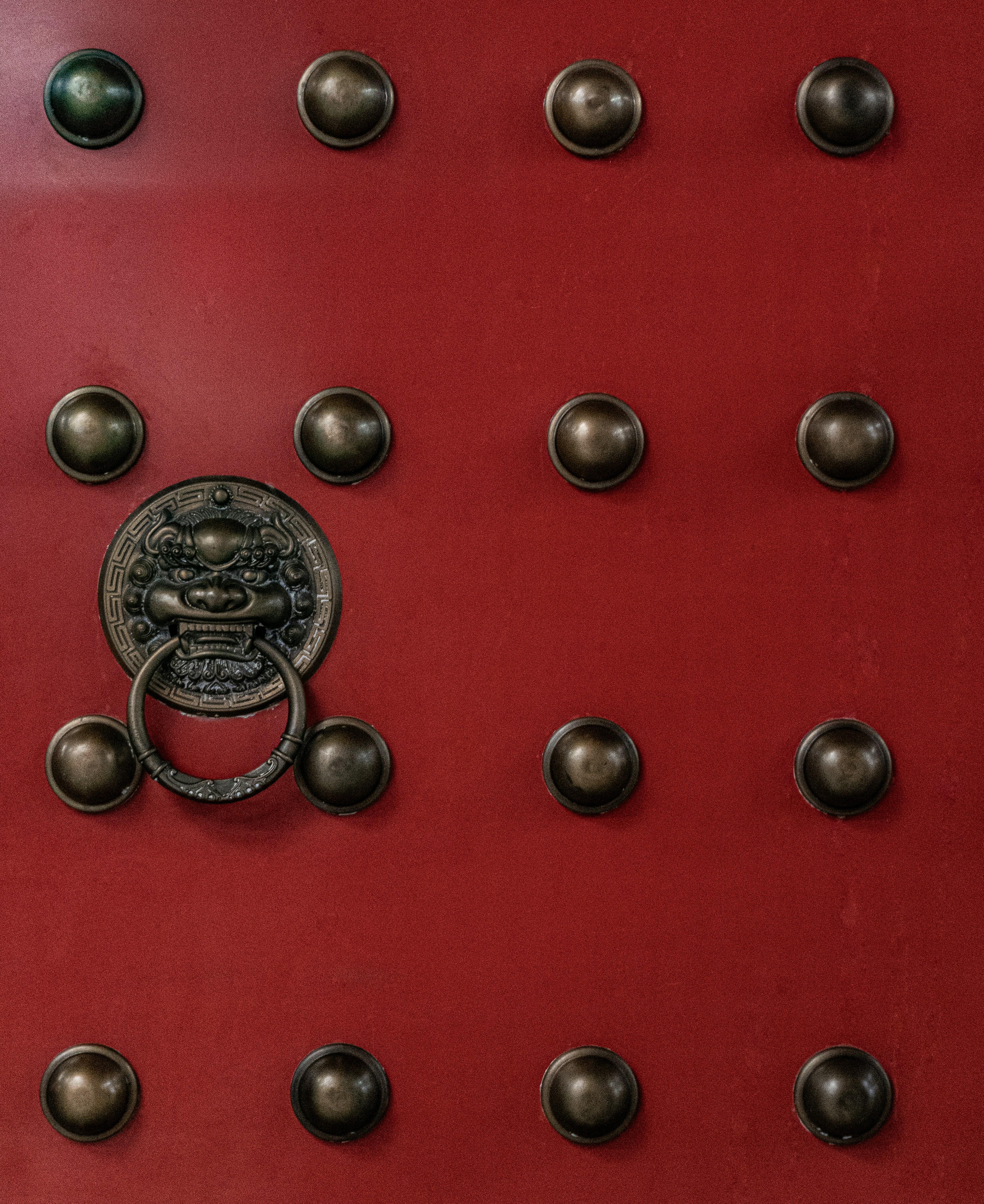 Crimson Studded Portal: Circular Knocker on a Weathered Red Door
