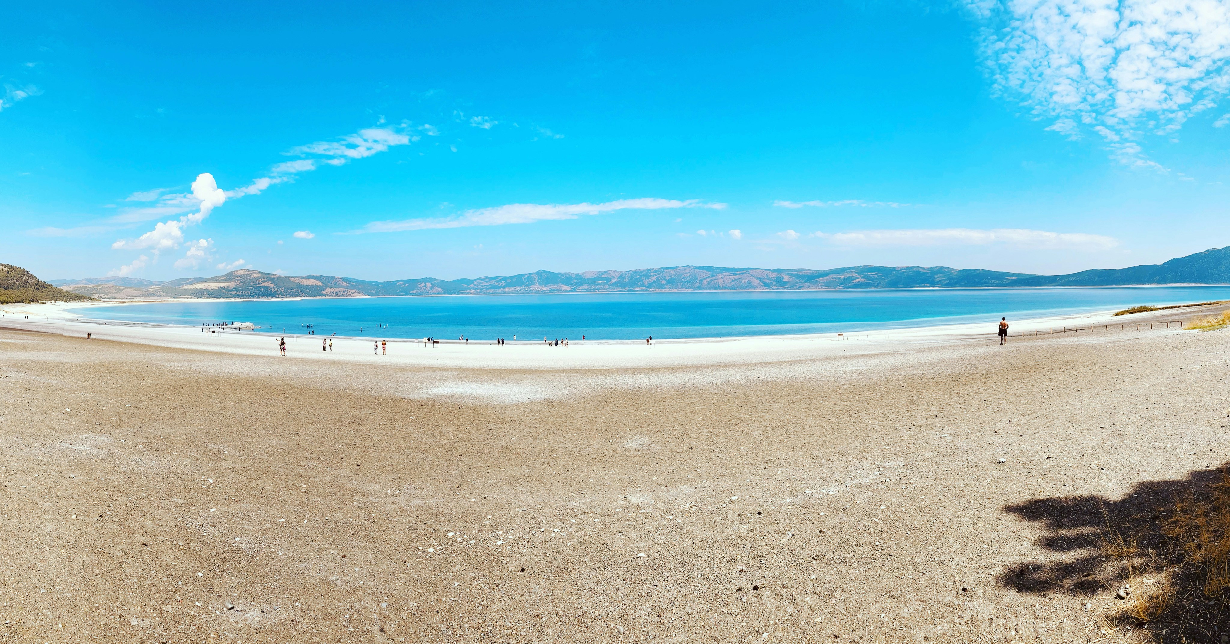 Vast sandy beach curving along a tranquil blue lake under a vibrant sky.