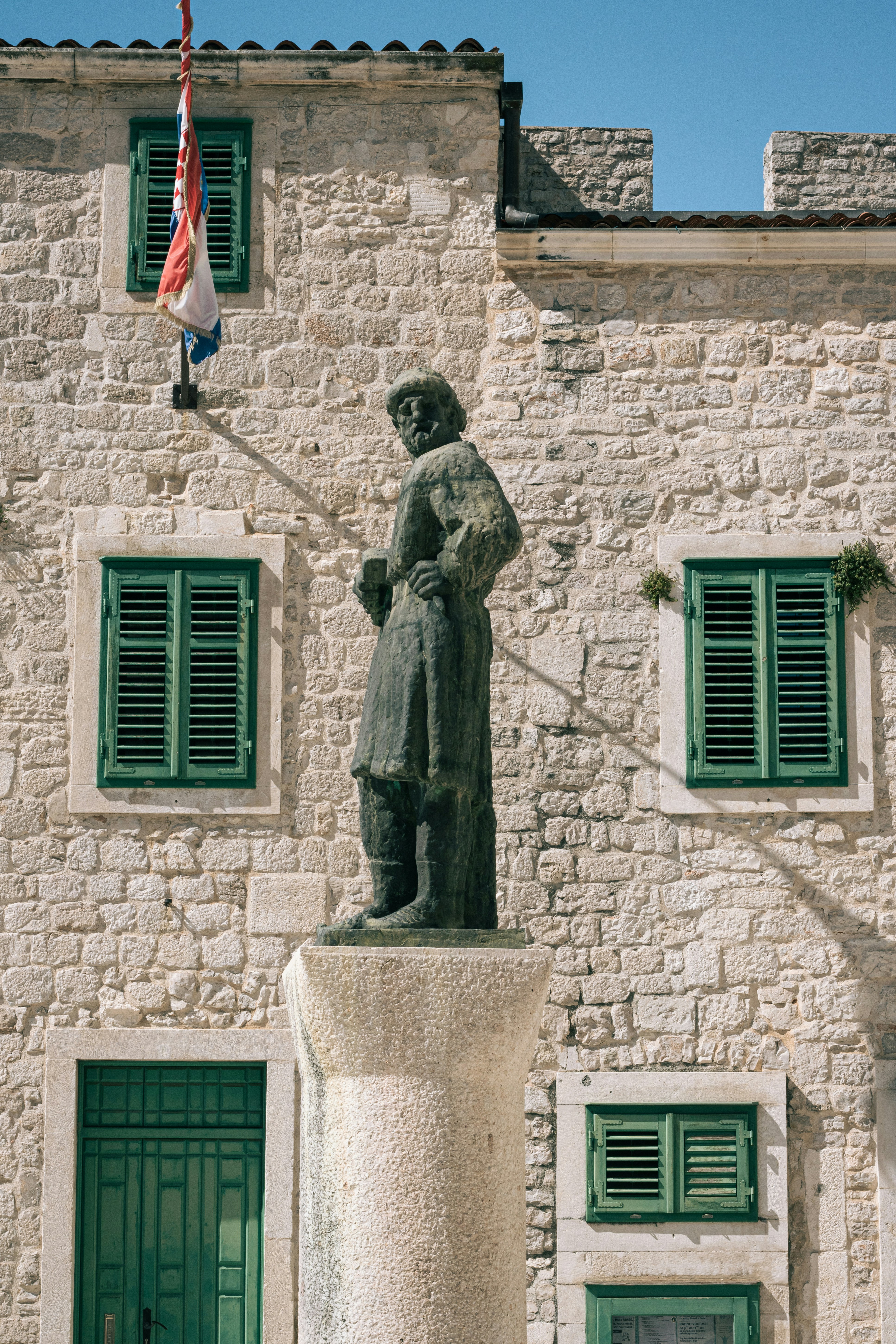 Stone Sentinel Before the Green-Shuttered Facade
