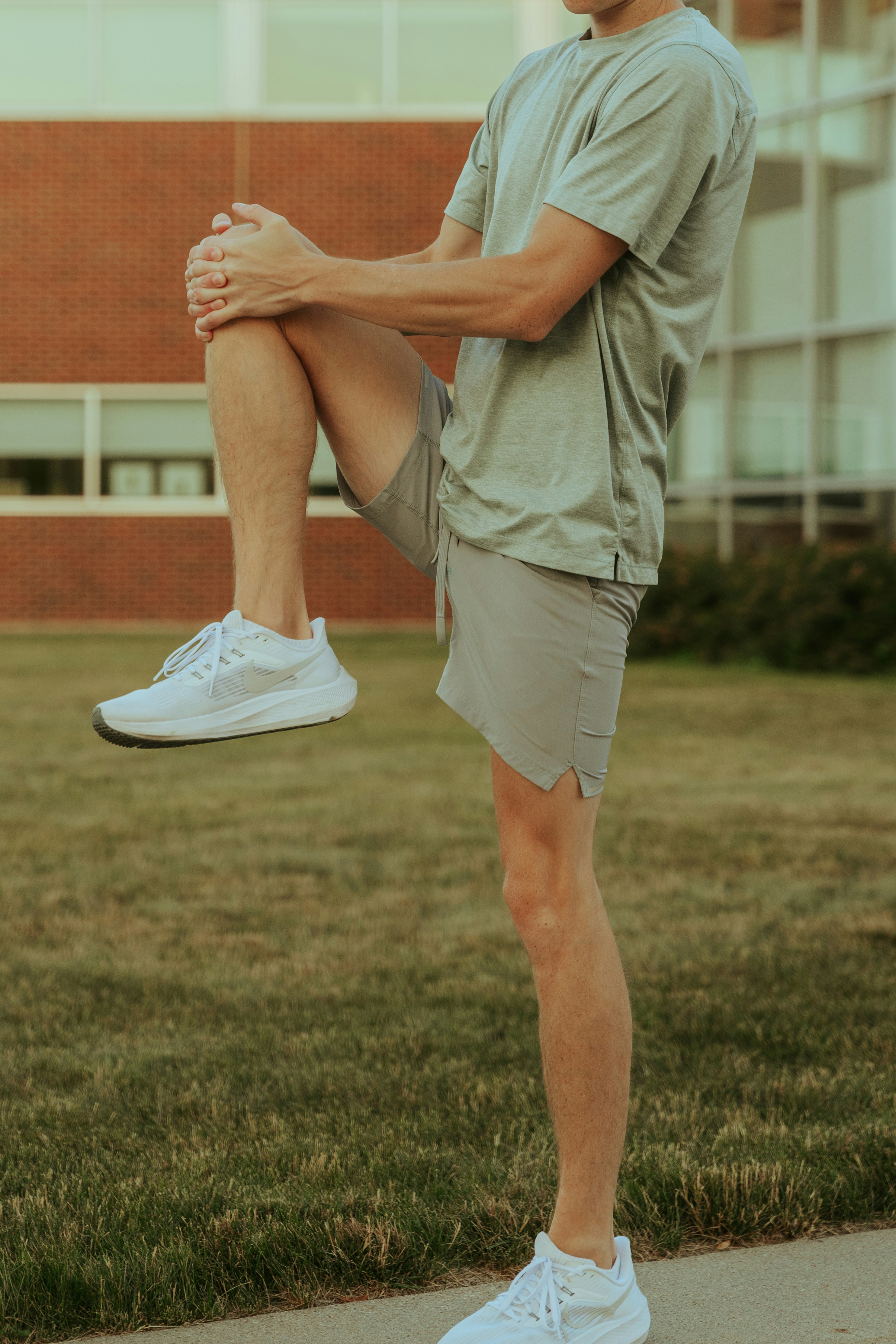 Athlete performing a dynamic stretch outdoors, showcasing athletic wear and a focus on mobility. Background features a modern building with soft lighting.