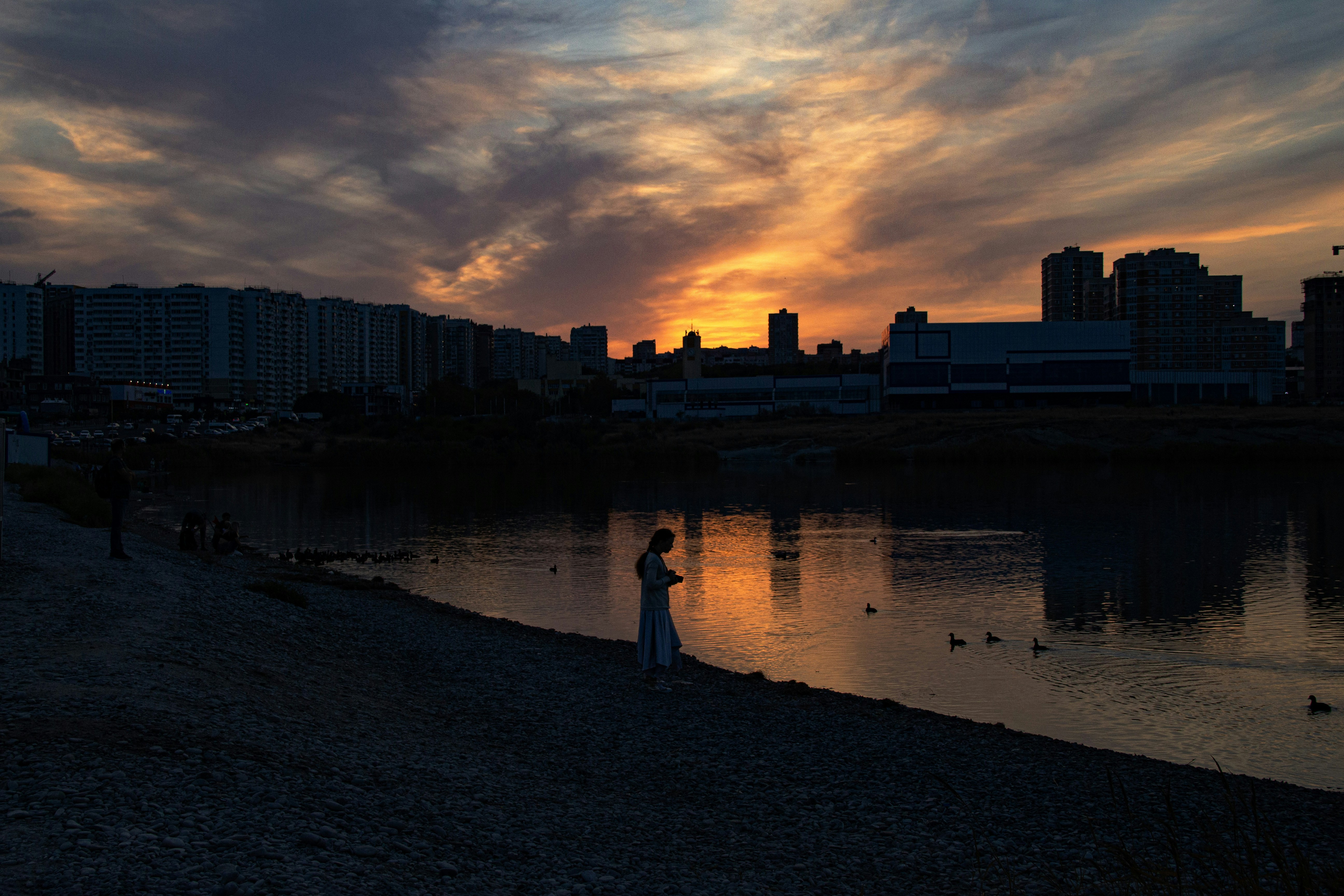 Silhouetted skyline against a vibrant sunset with reflections on calm water.