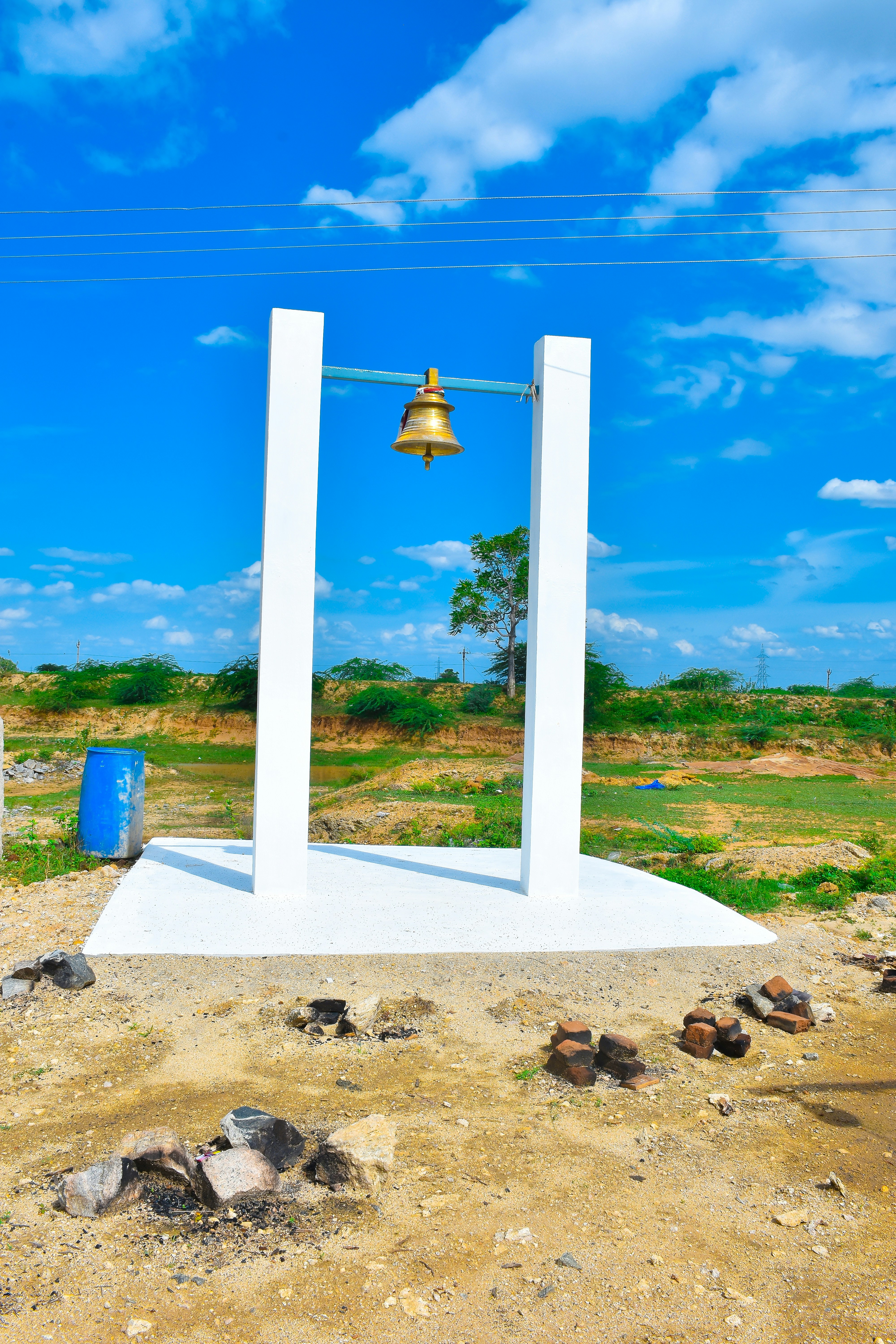 A solitary bronze bell suspended within a stark white frame under a bright desert sky