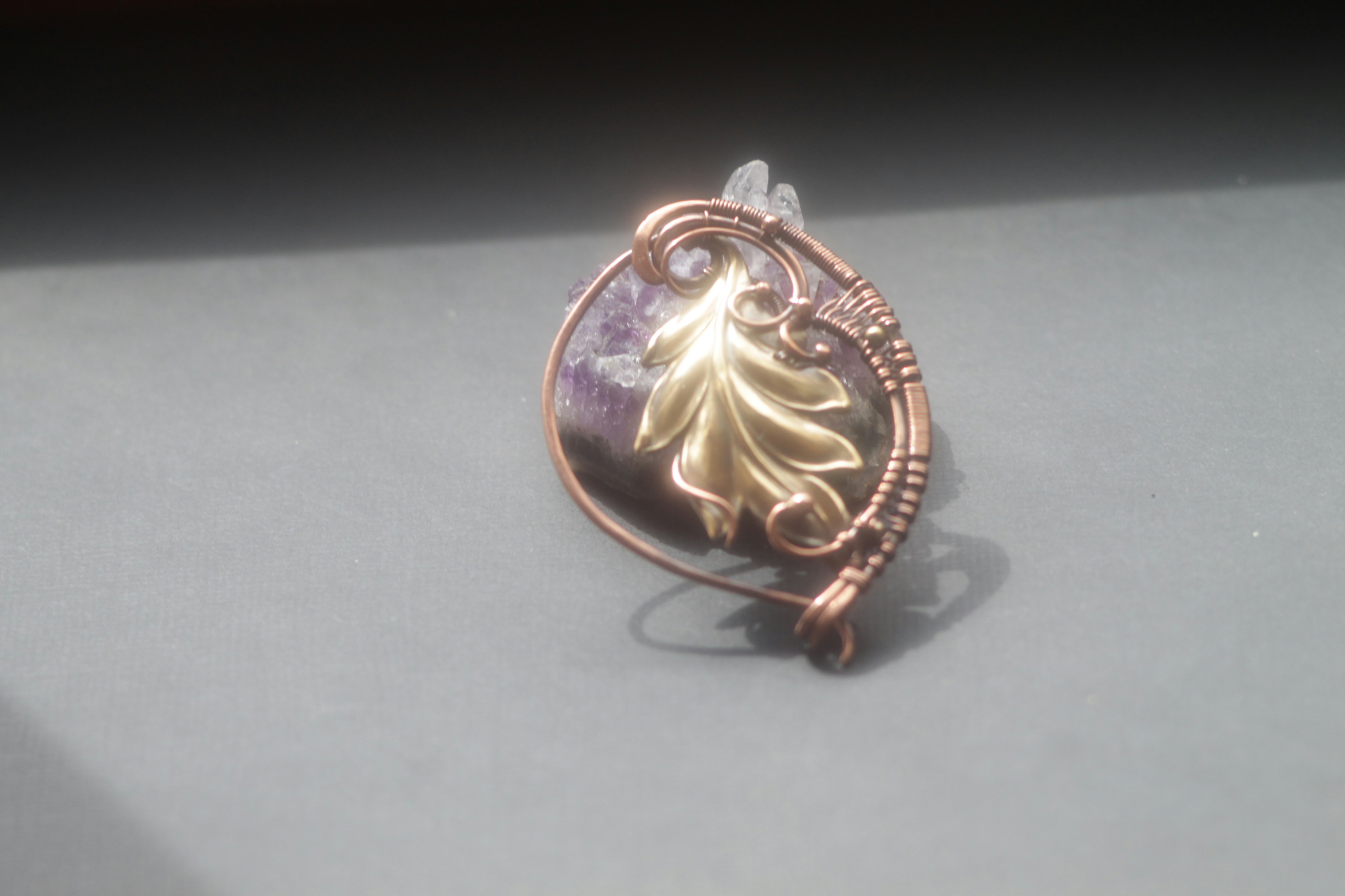 Copper Leaf Pendant with Amethyst Orb on a Quiet Surface