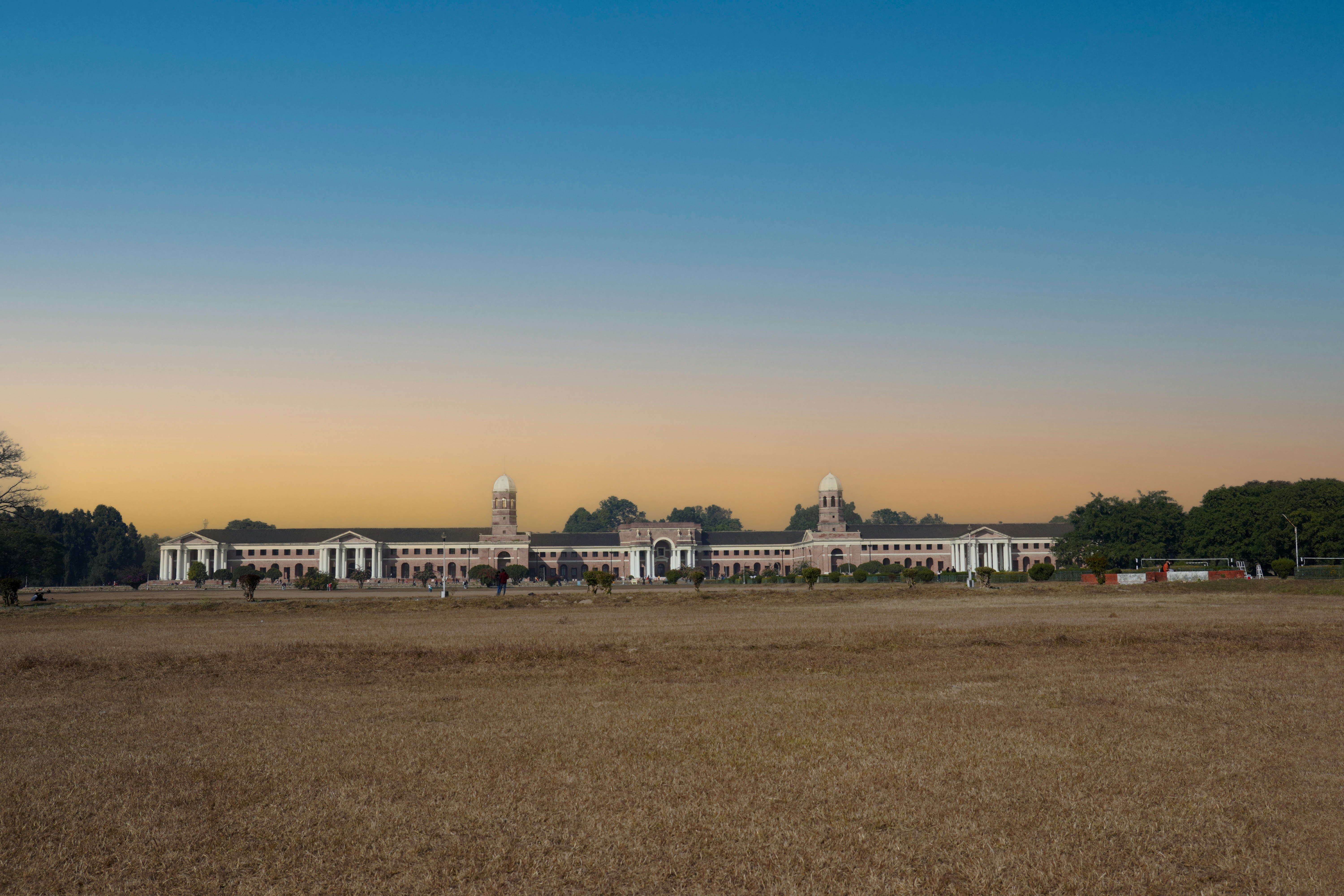 Expansive field with distant historic buildings under a clear sunset sky.
