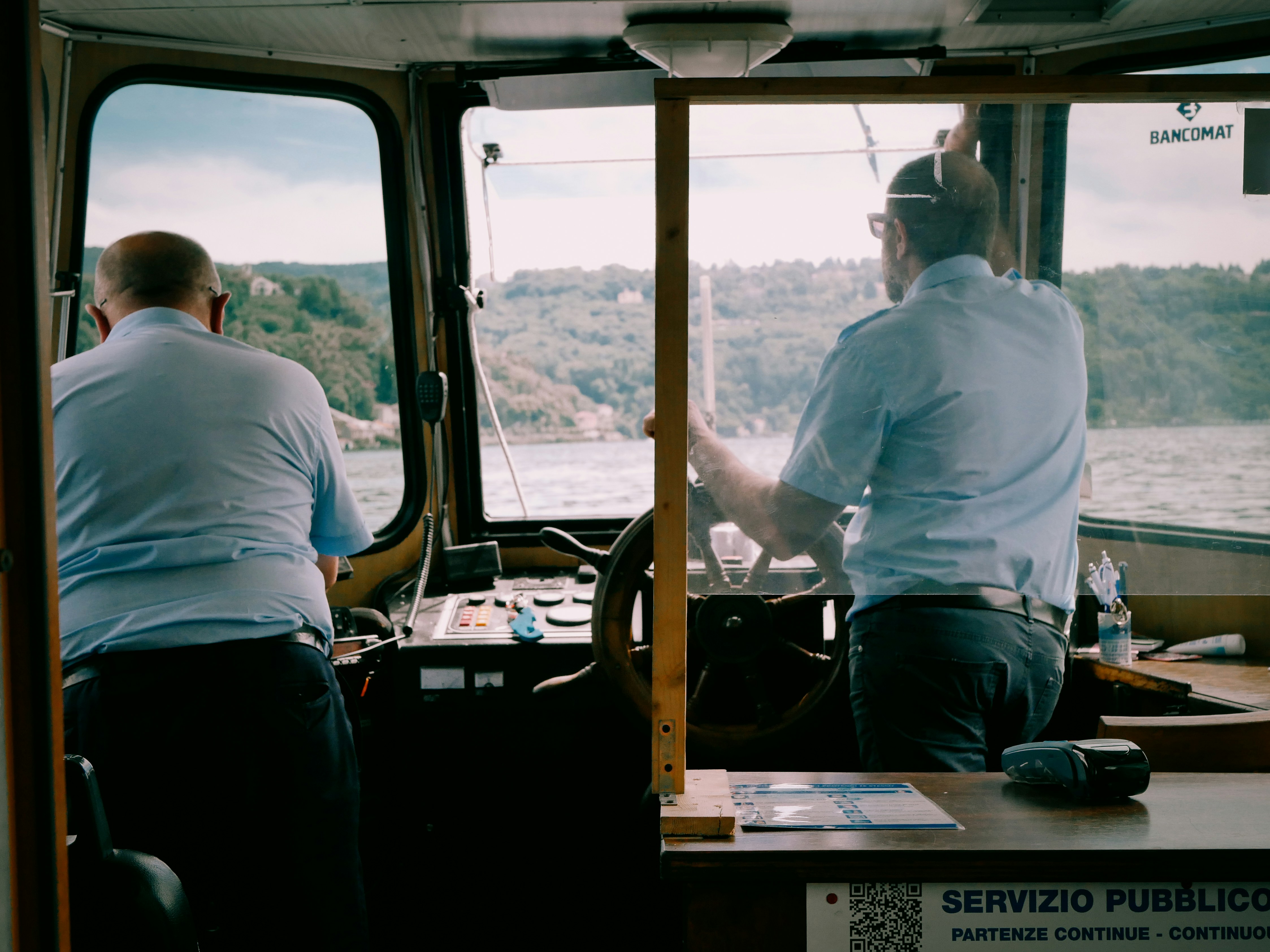 At the Helm: Two Crew in Light Blue Overlooking a Tranquil River