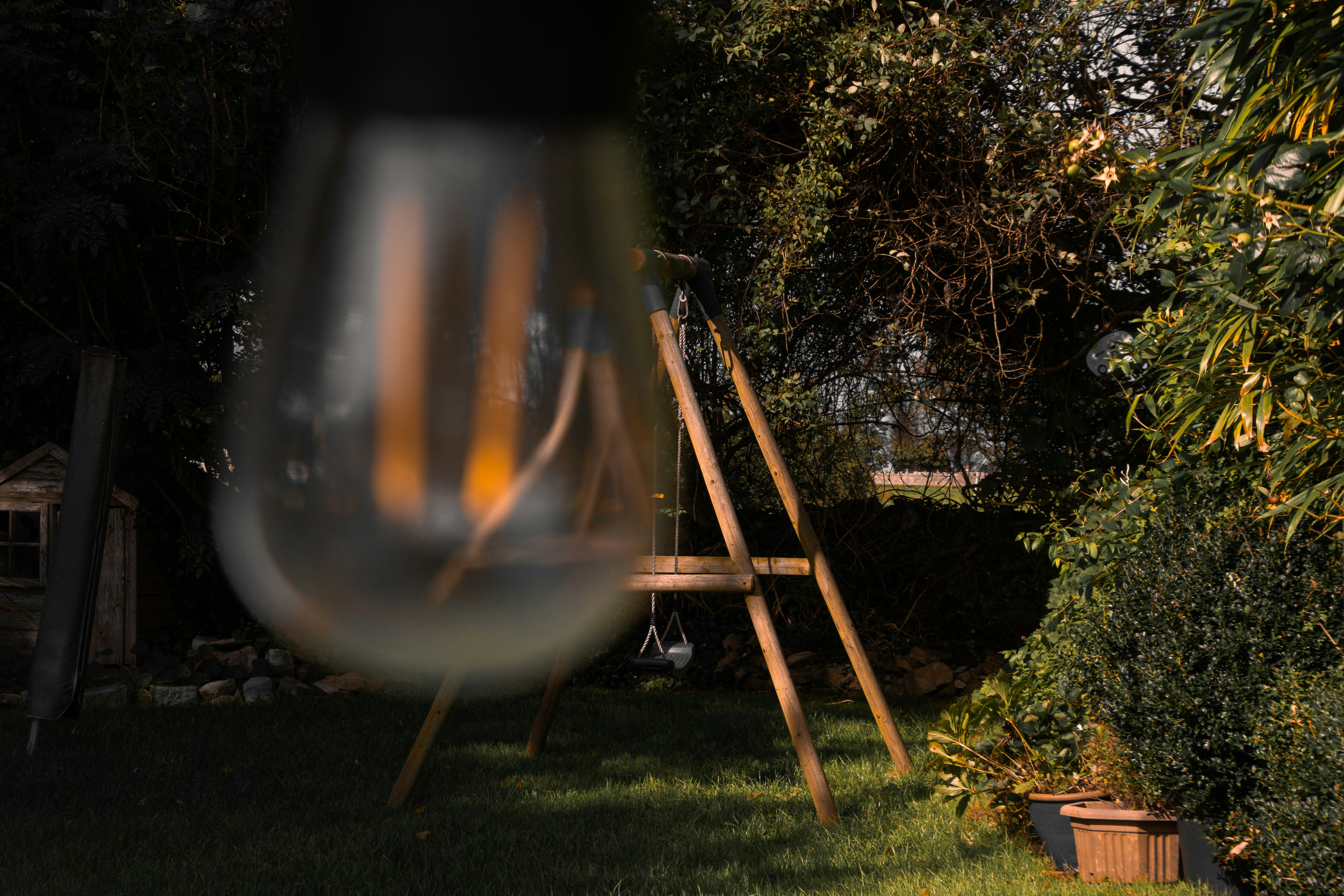 Gone Glass: a blurred lantern foreground with a wooden swing set in a quiet backyard