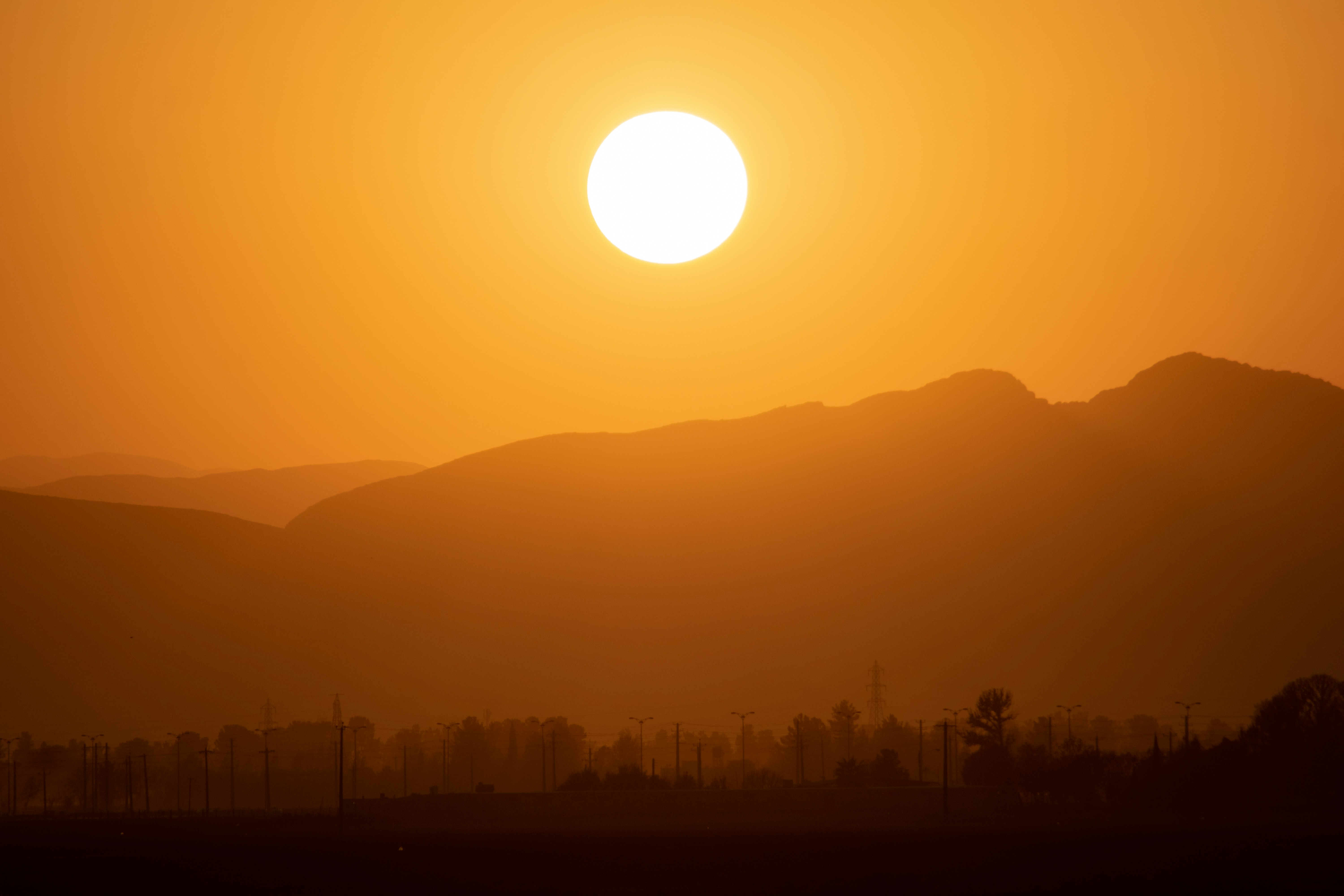 Sun setting over a silhouetted mountain range with a warm orange sky.