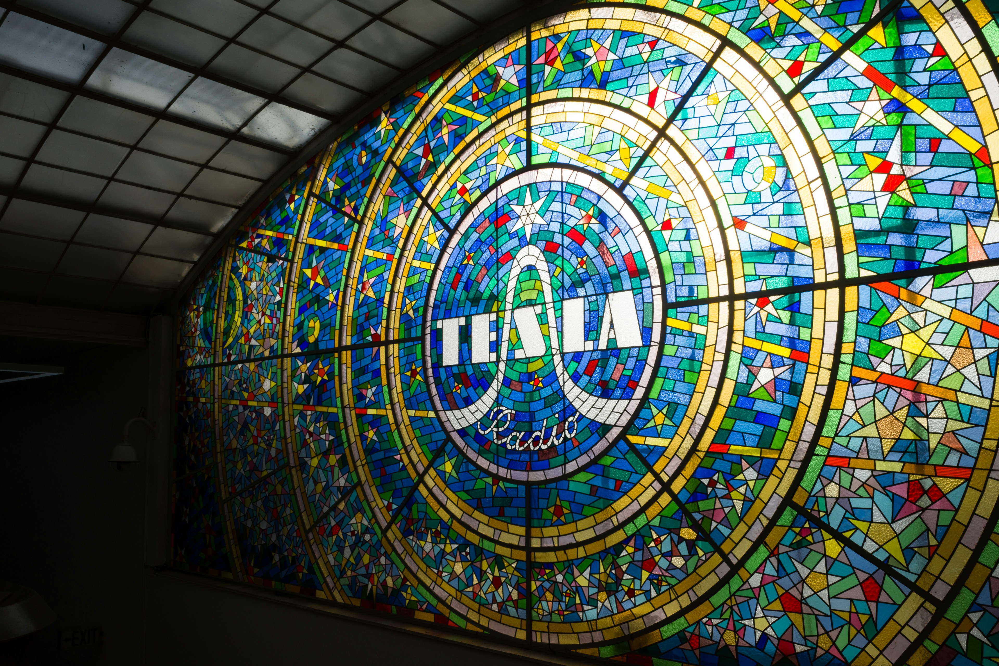Circular Stained-Glass Mosaic Framing the Tesla Radio Emblem in a Dim Corridor