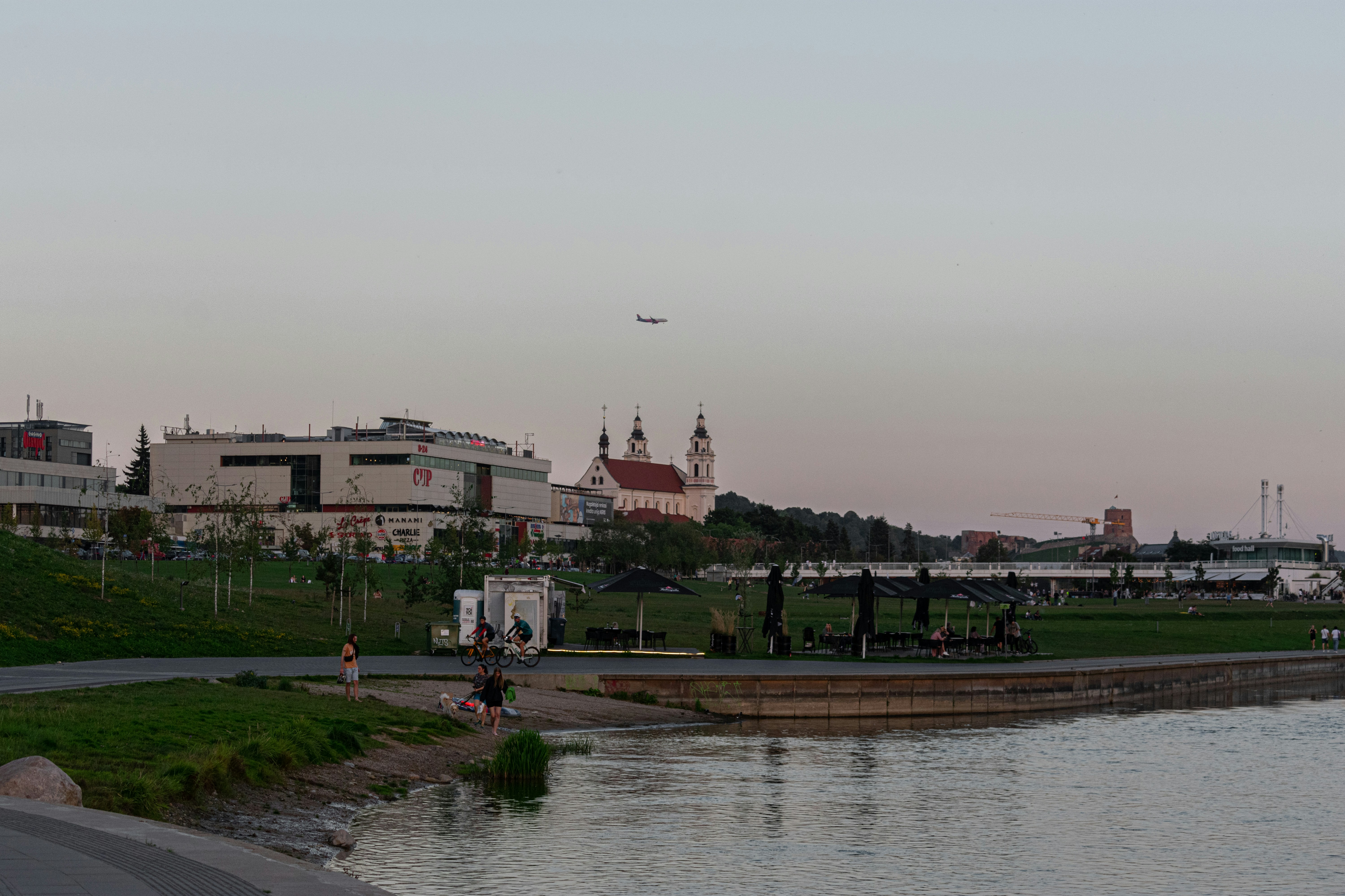 Evening view of a riverside cityscape with a historic church and modern buildings under a pastel sky.