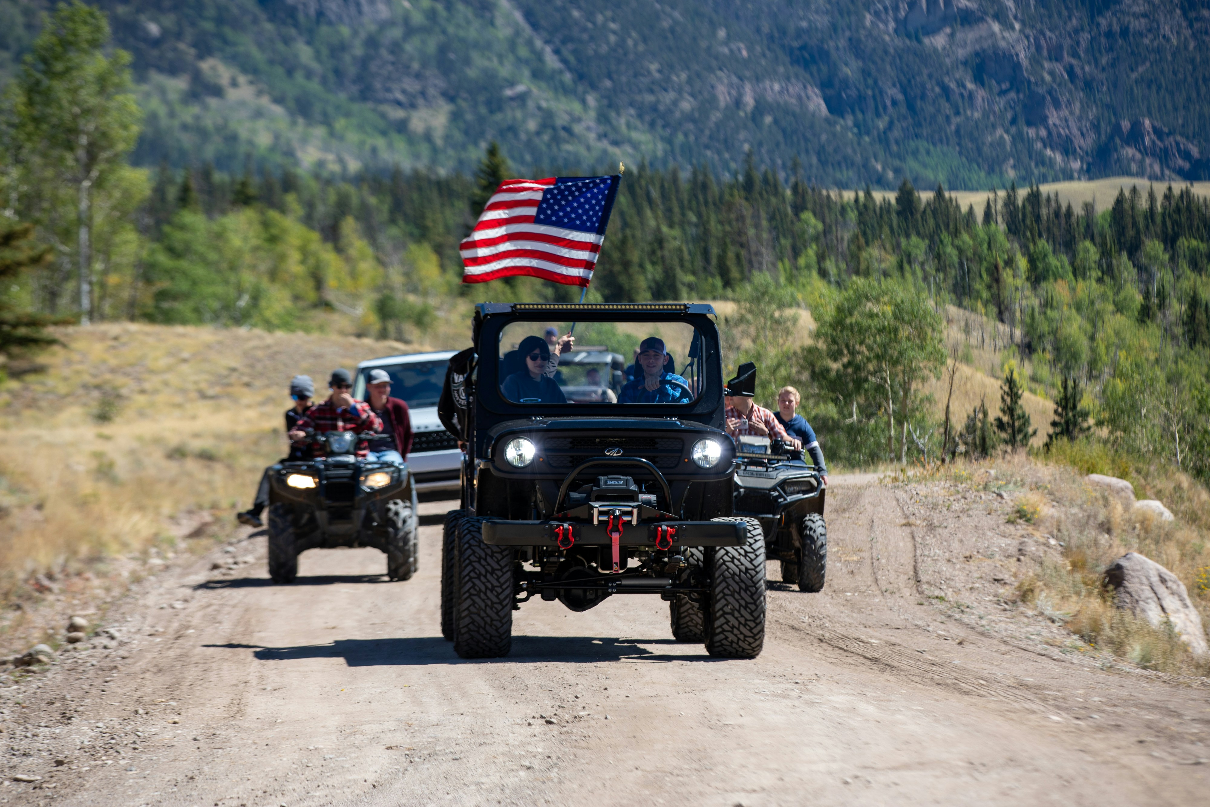 A group of people riding on the back of four wheelers down a dirt road ...