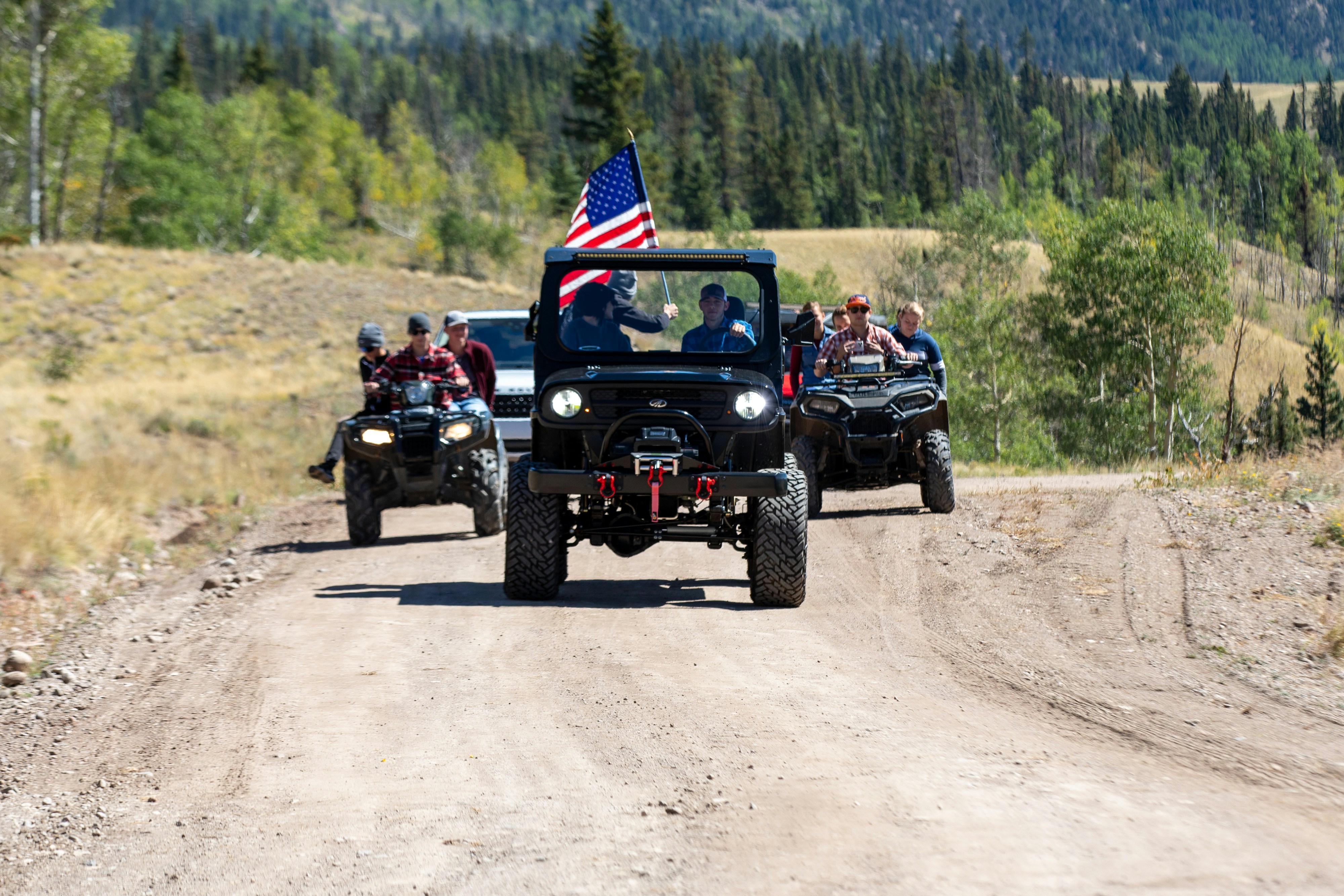 A group of people riding on the back of four wheelers down a dirt road ...