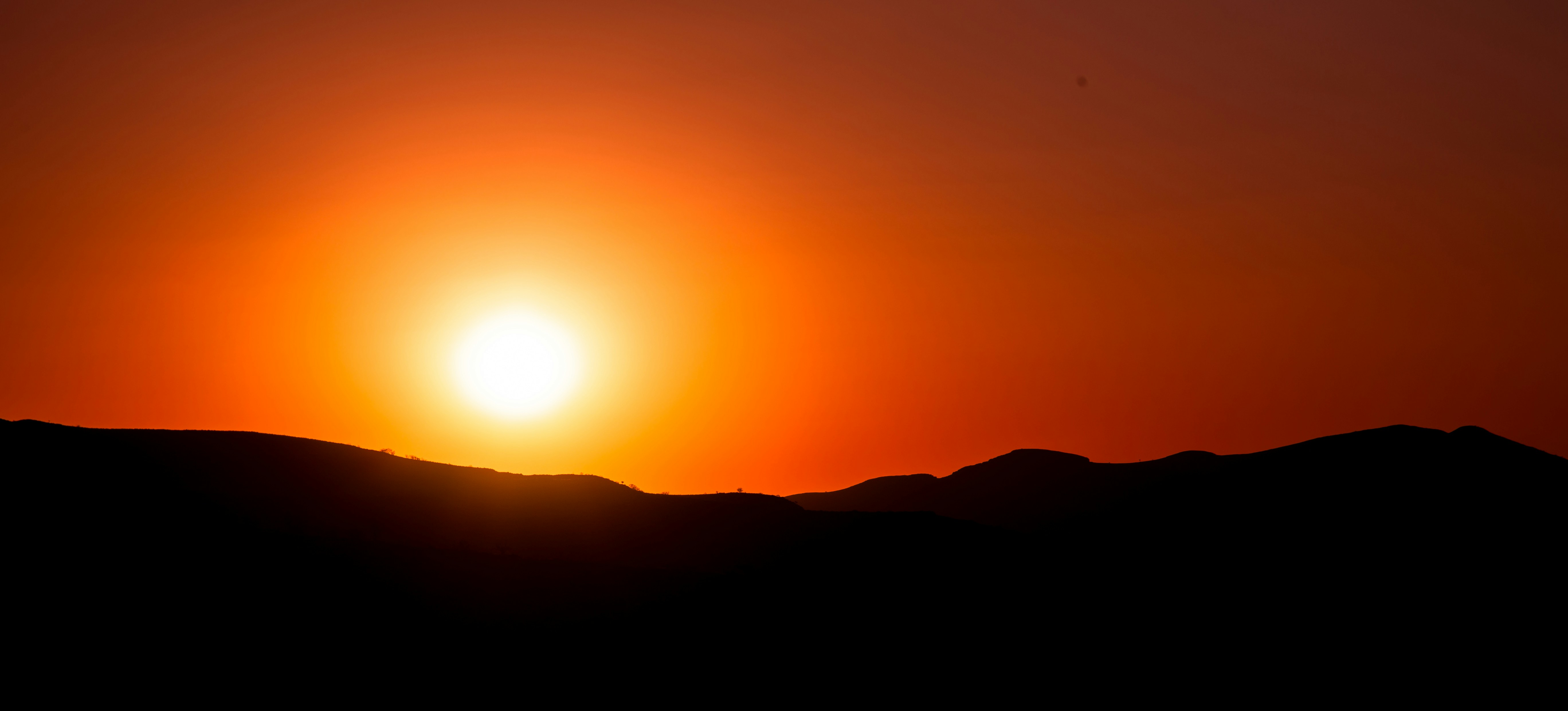 Golden sun setting behind a silhouette of rolling hills, casting a warm glow across the sky.