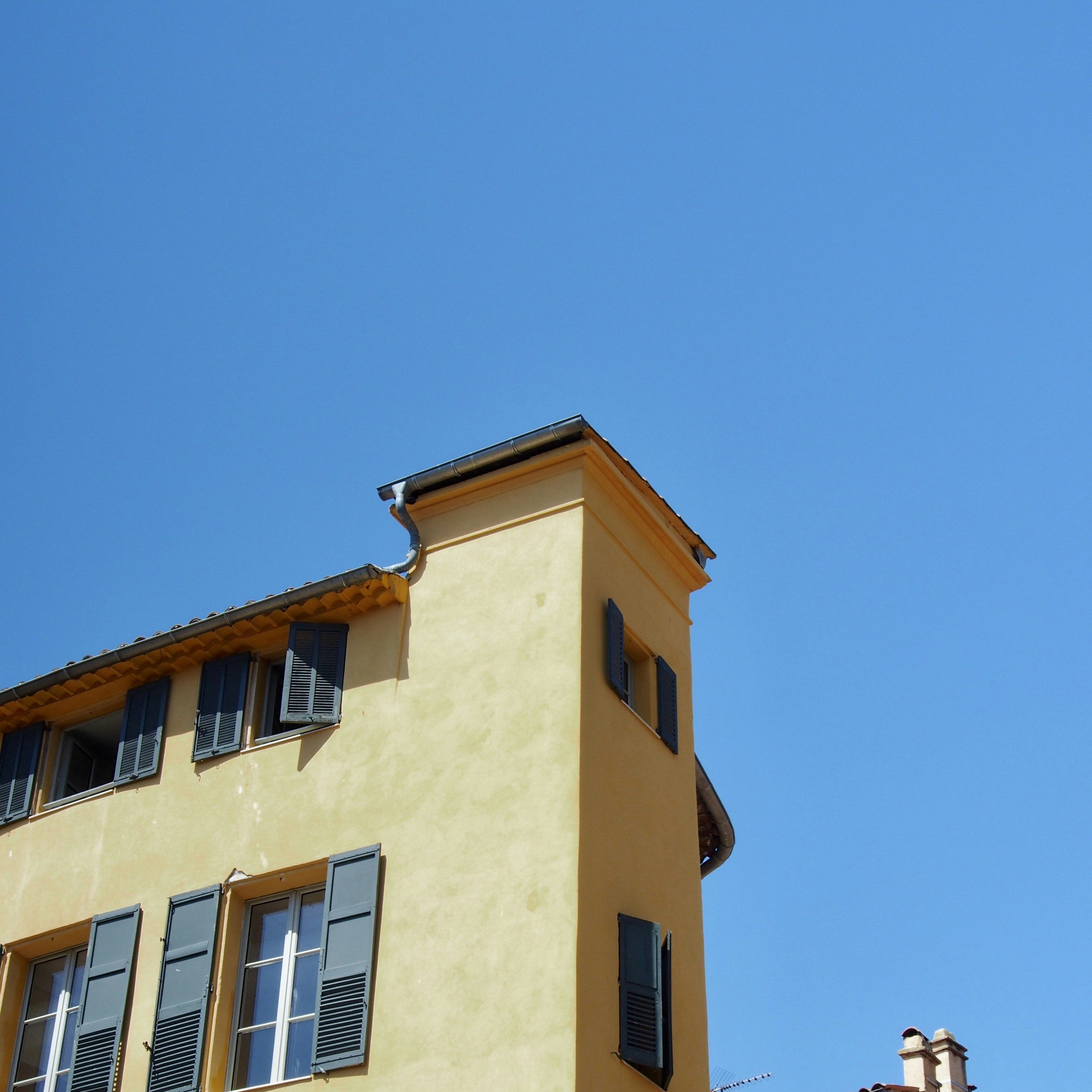 A tall yellow building with black shutters and windows photo – Free ...