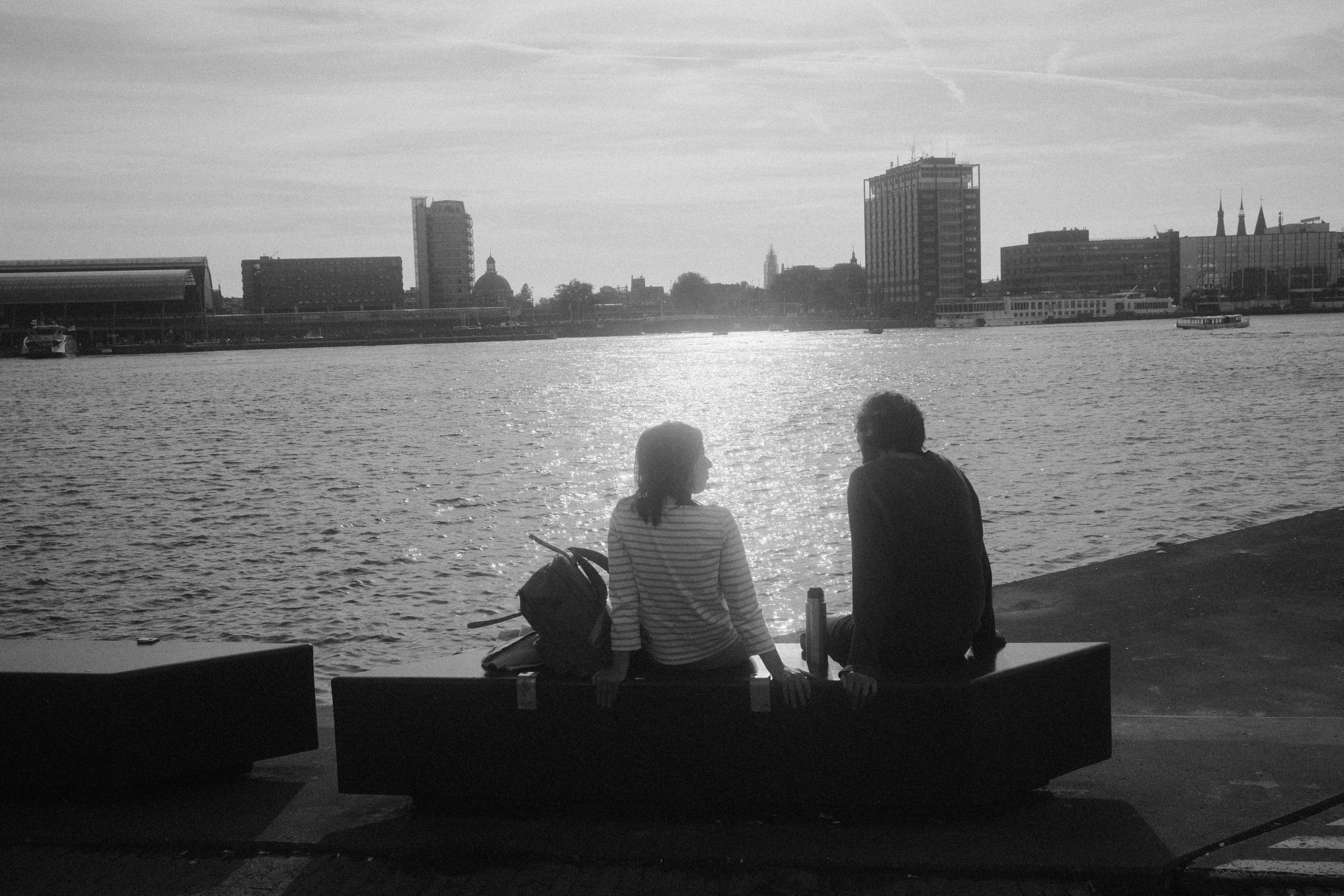 Riverside Quiet: Two Silhouettes on a Bench as City Lights Reflect on the Water