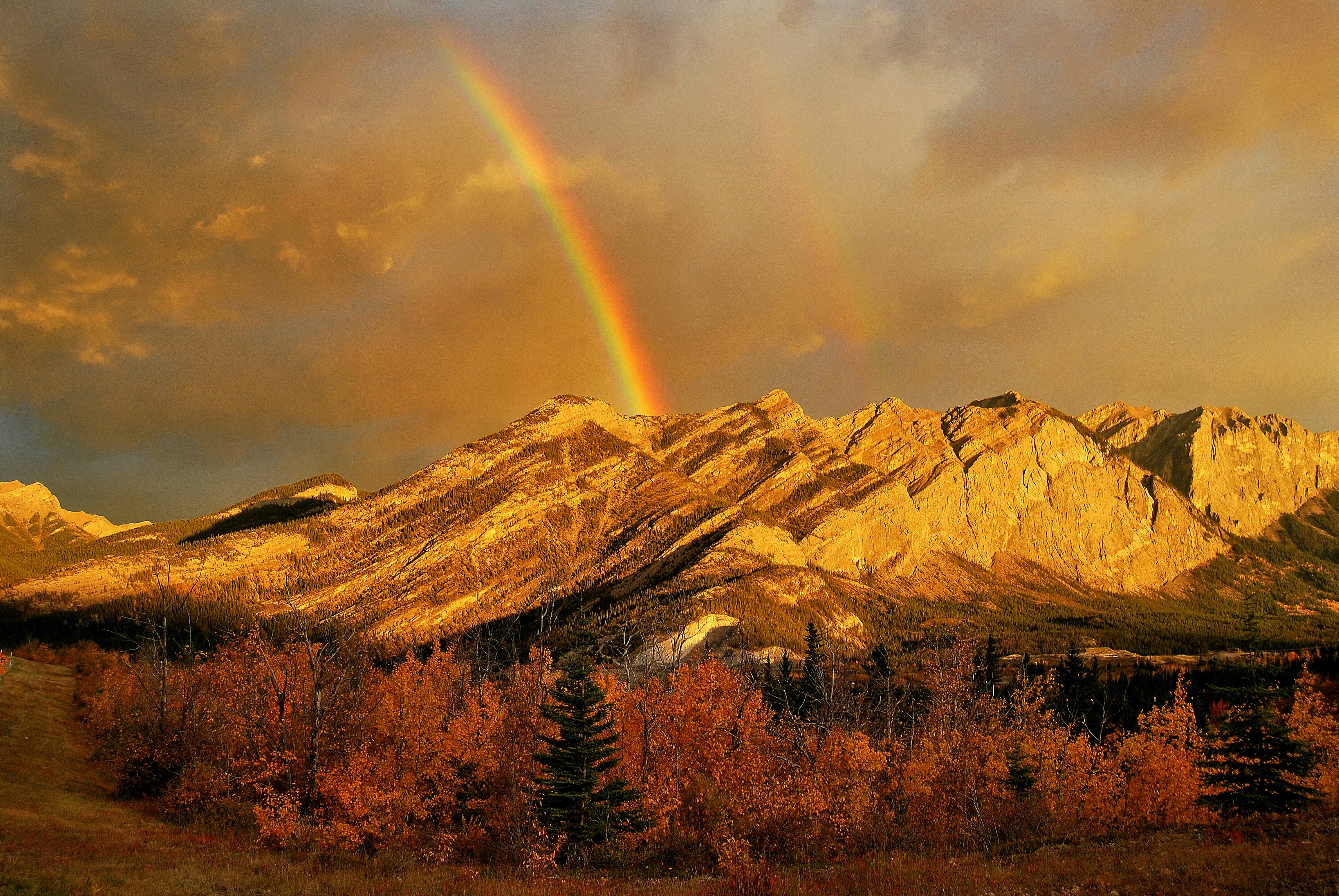 Golden Peaks beneath a Curve of Color: A Mountain Landscape with a Rainbow