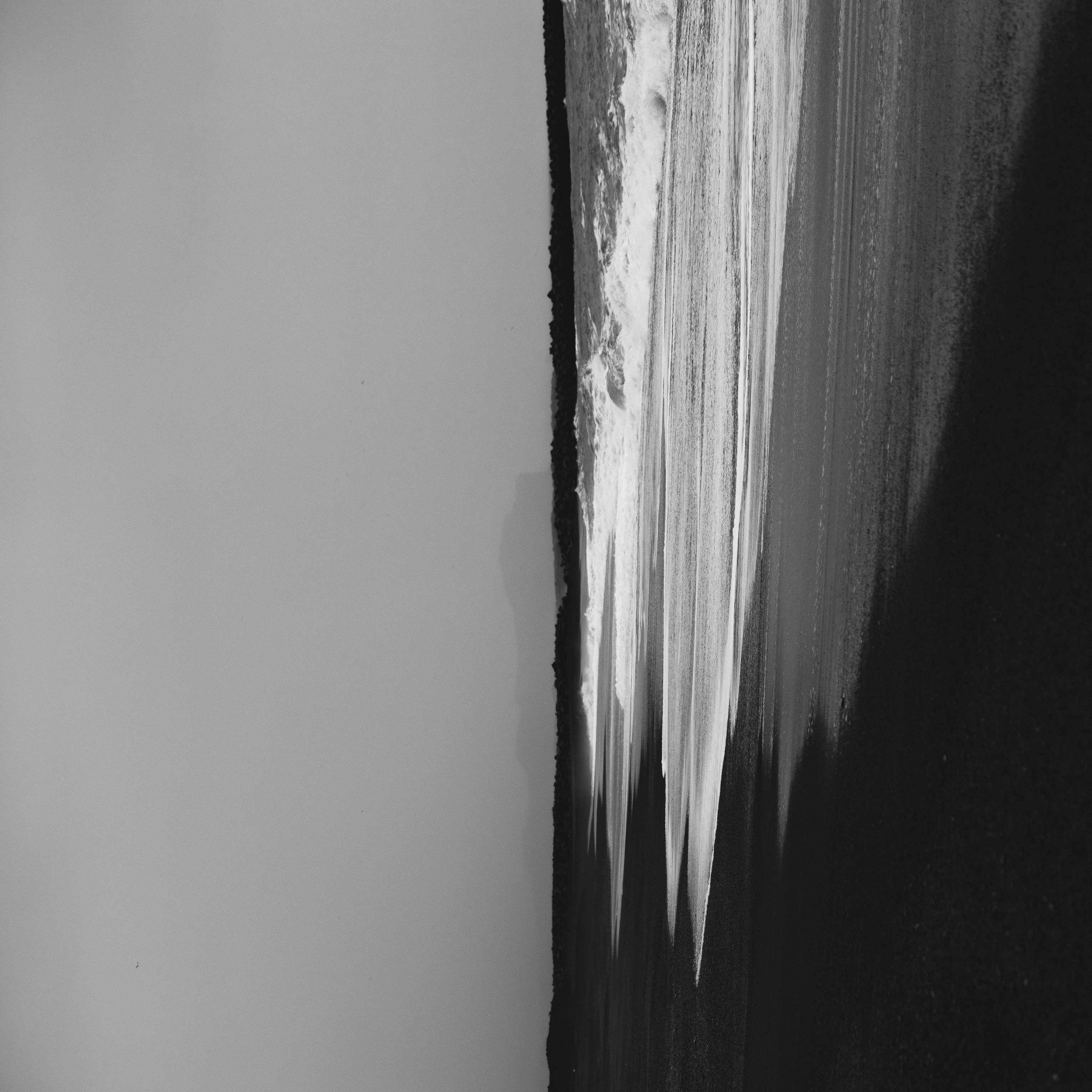 Gentle waves caress a dark, sandy beach under soft light, creating a serene contrast between land and sea.