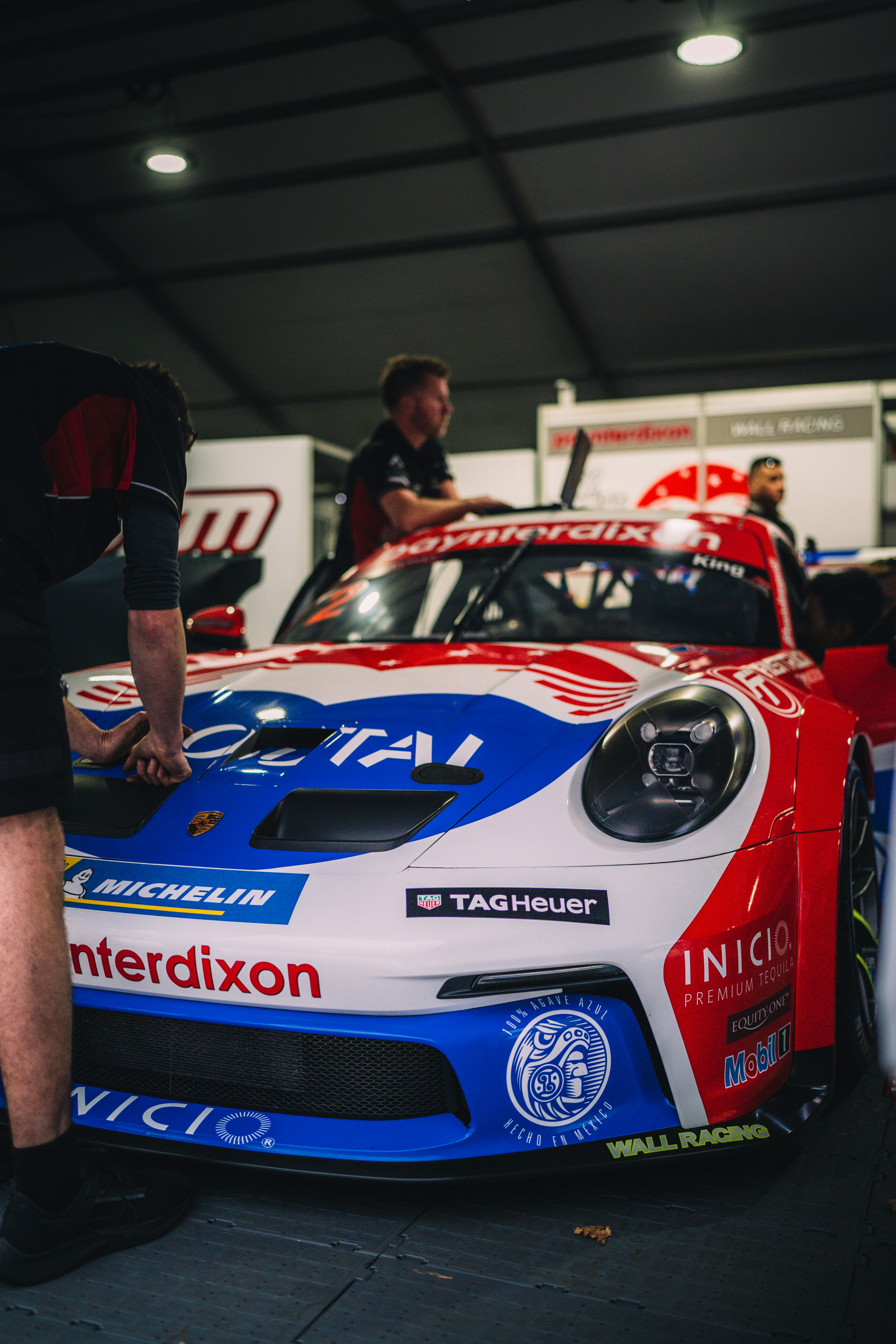 Porsche NASCAR in a busy pit—colorful race livery and crew at the ready