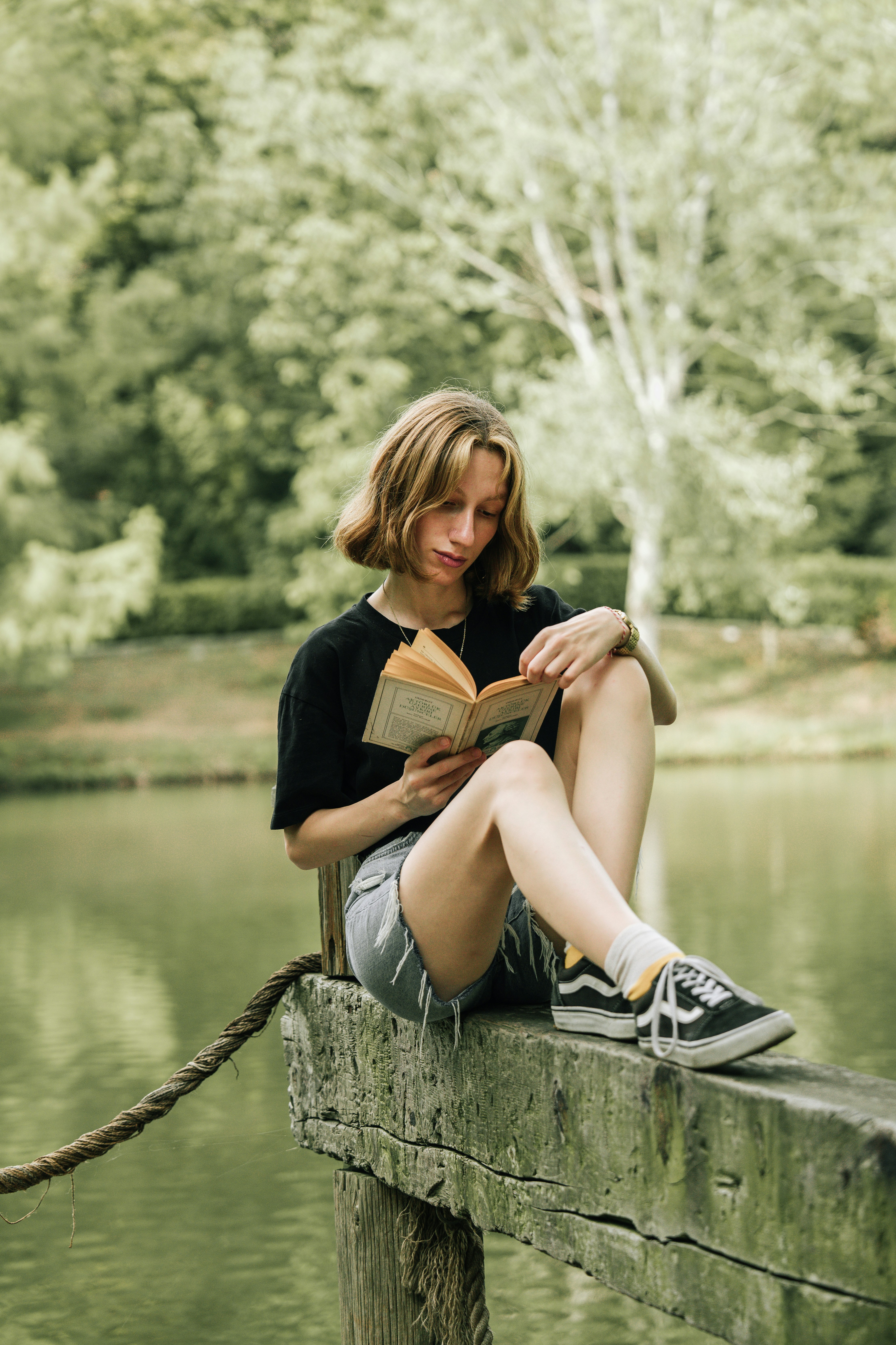 A woman sitting on a dock reading a book photo – Free Person Image on ...
