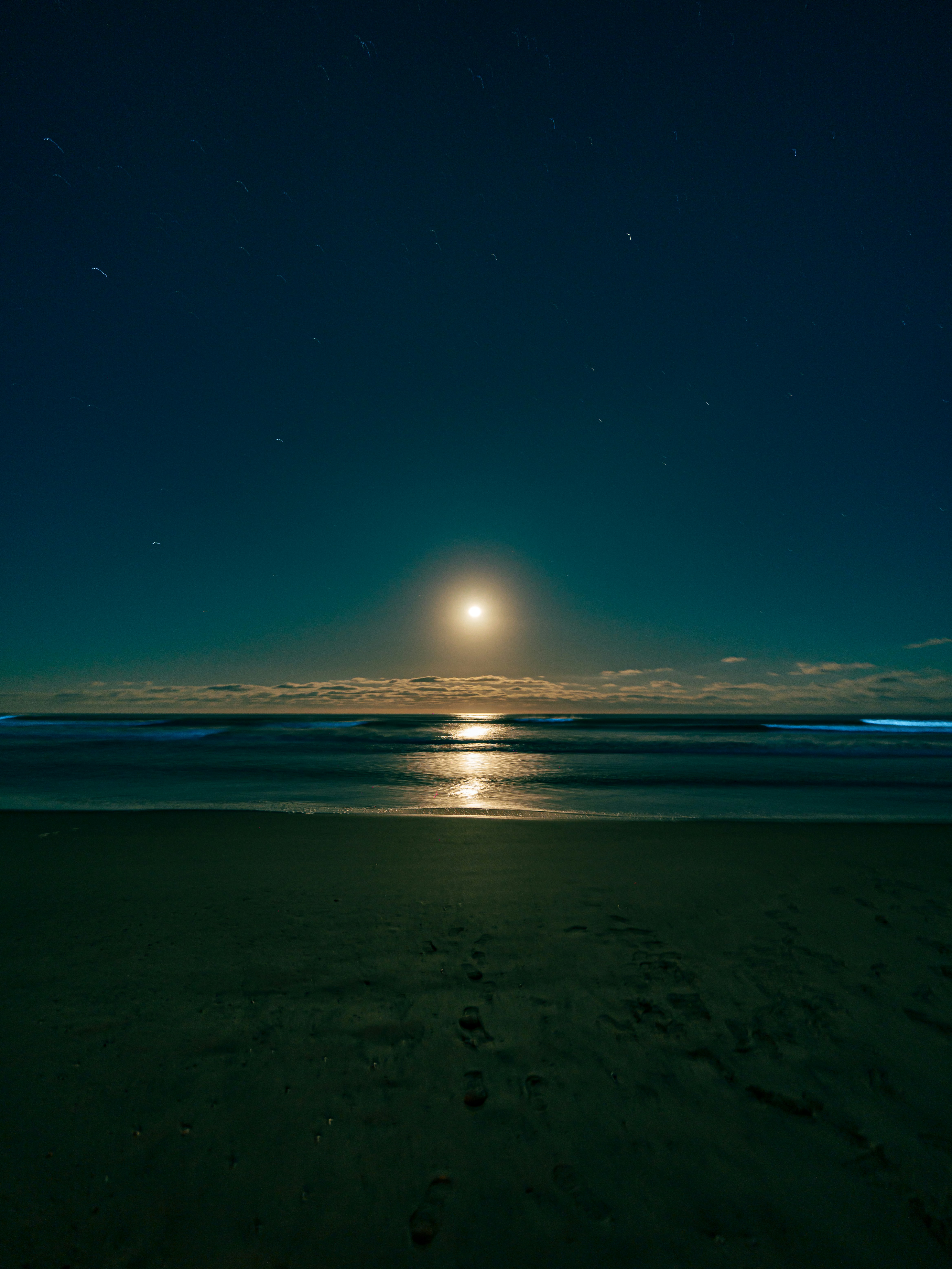 A full moon setting over the ocean with a beach in the foreground photo ...