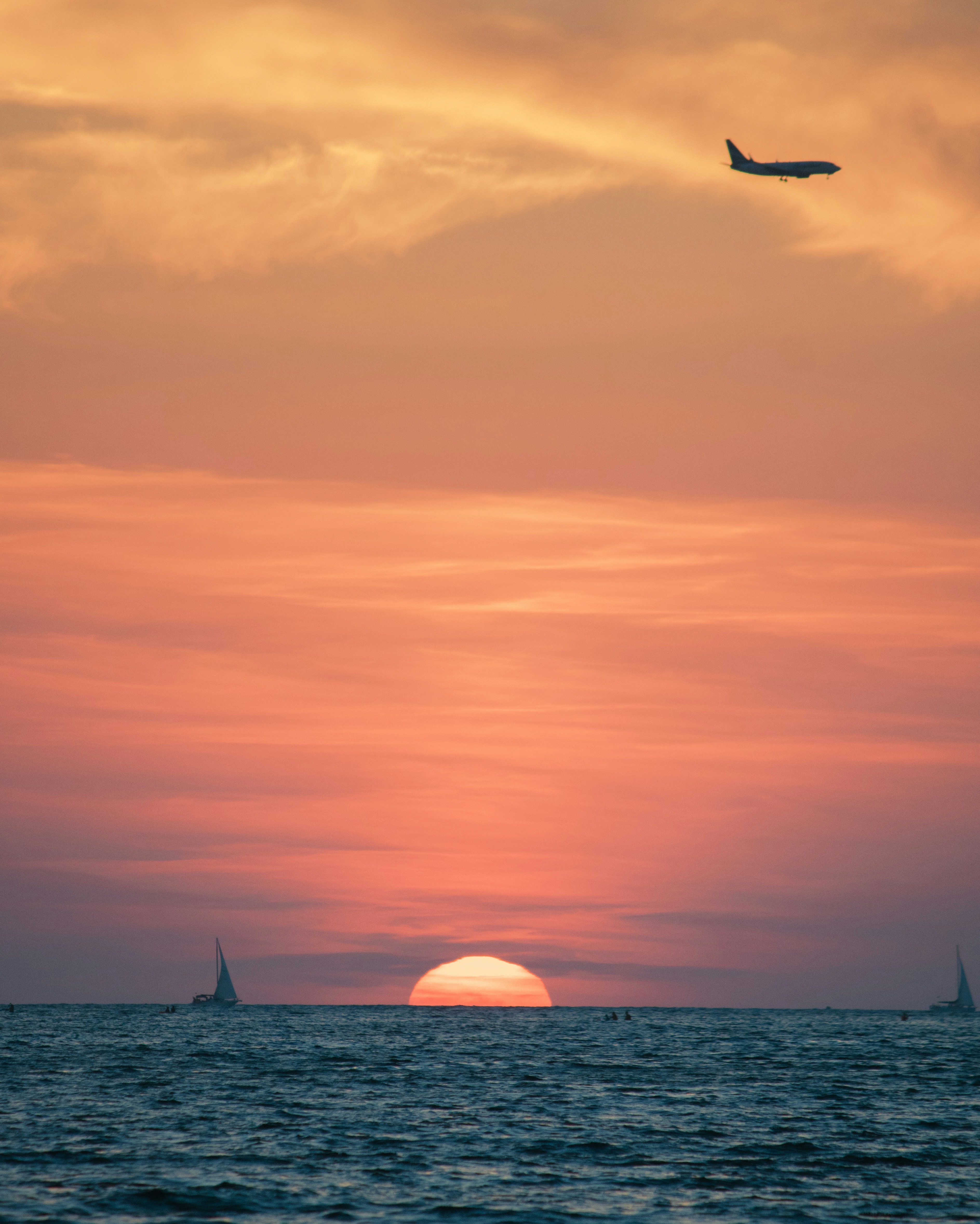 Sunset at the Quiet Horizon: Sun Dips Behind the Sea as a Plane Crosses the Sky